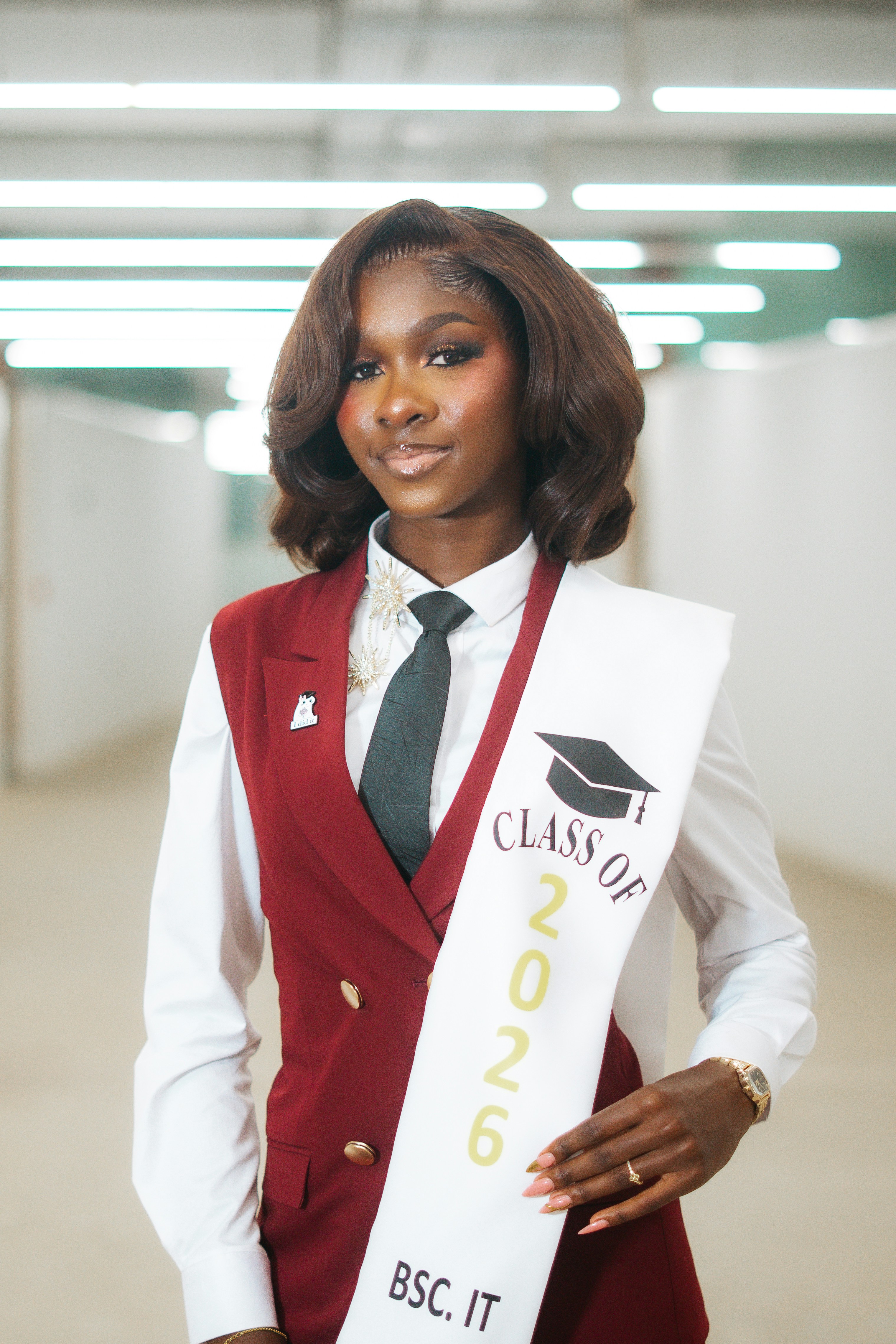 Graduate in White Shirt and Burgundy Vest Stands in Bright Corridor