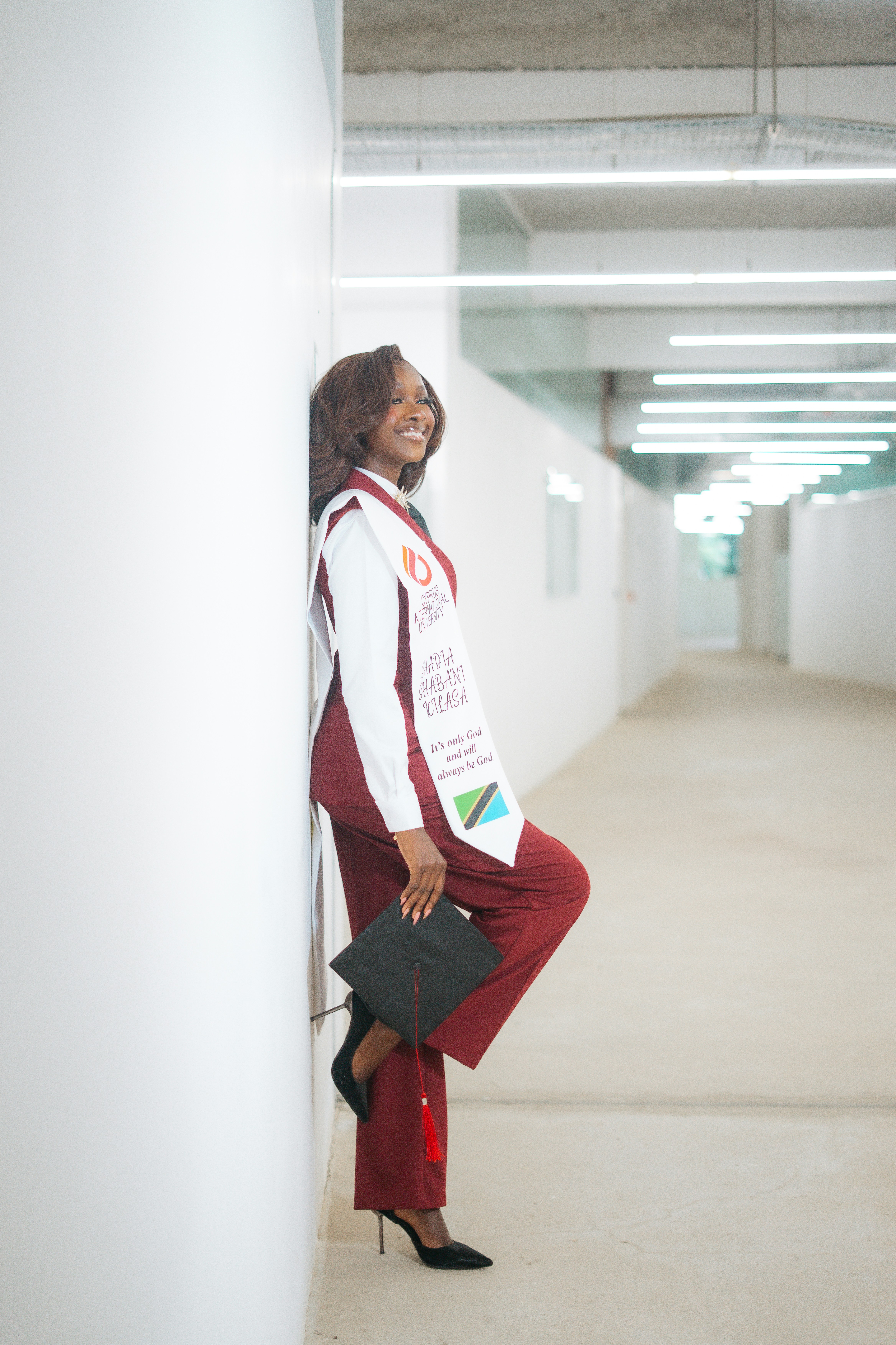 Graduation Portrait Lean: A hopeful graduate in a red-and-white gown rests against a bright hallway
