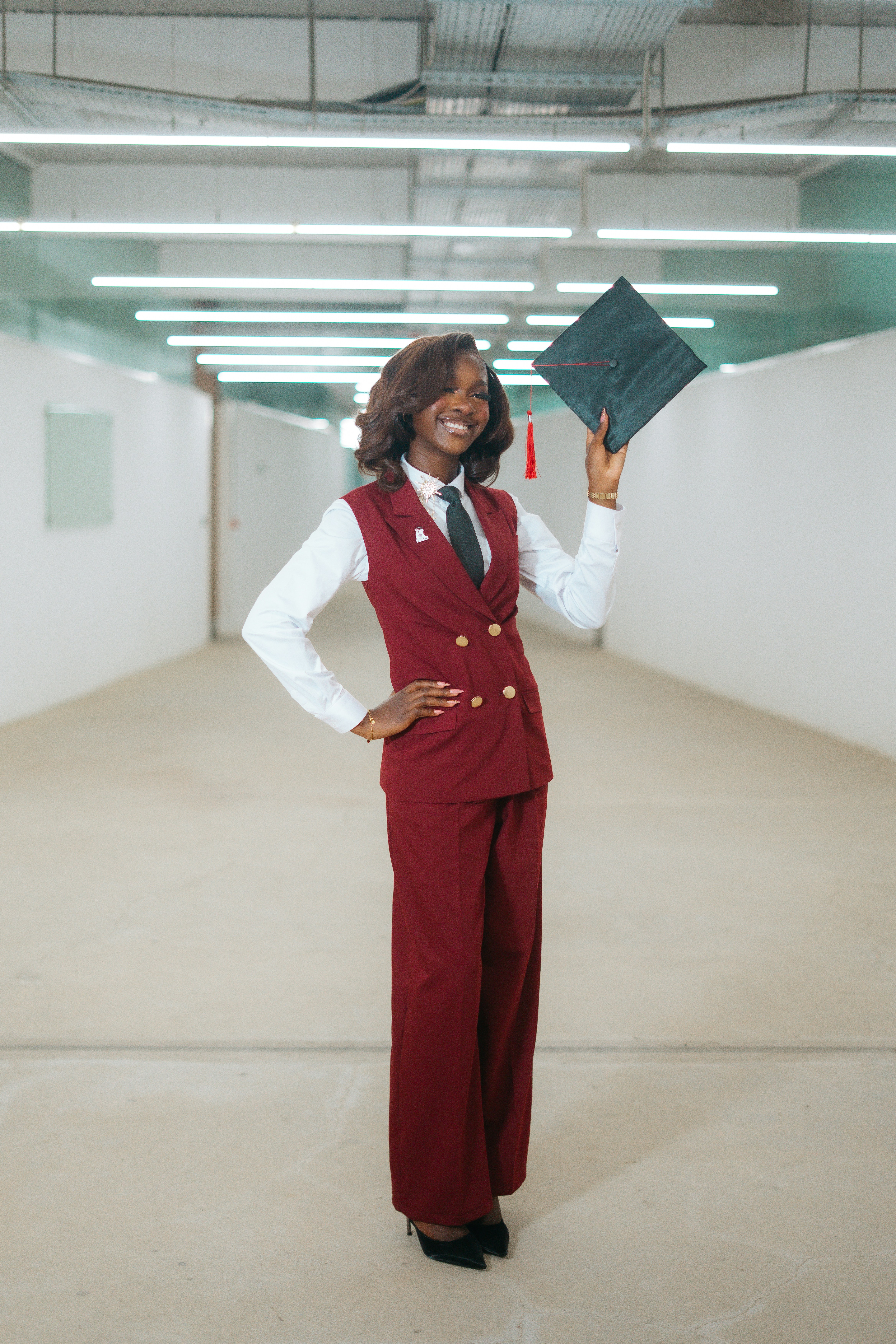 Graduate in Crimson: A Confident Pose Under Fluorescent Arches
