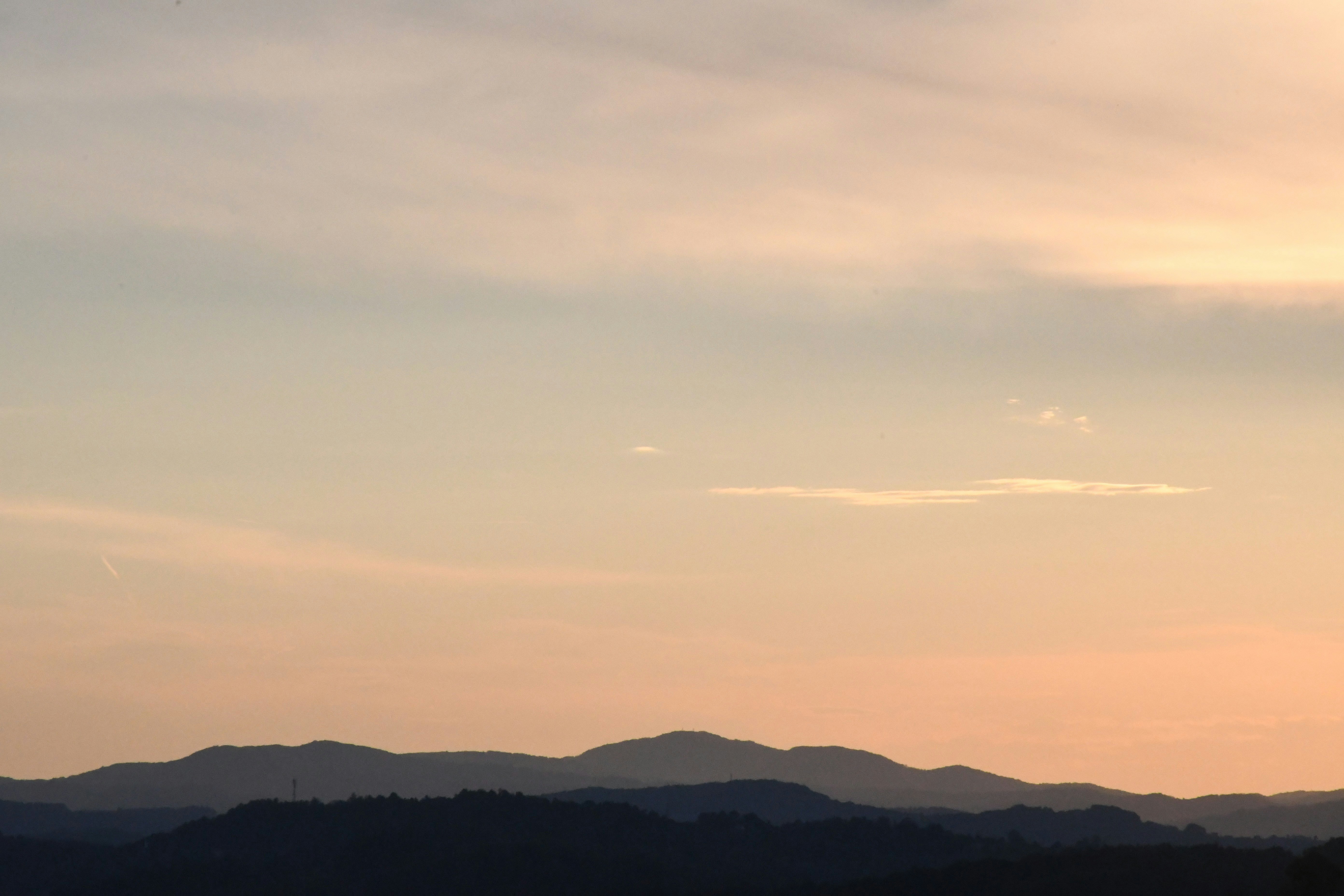 Distant Silhouette at Dusk: Layers of Hills Against a Peach-Soaked Sky