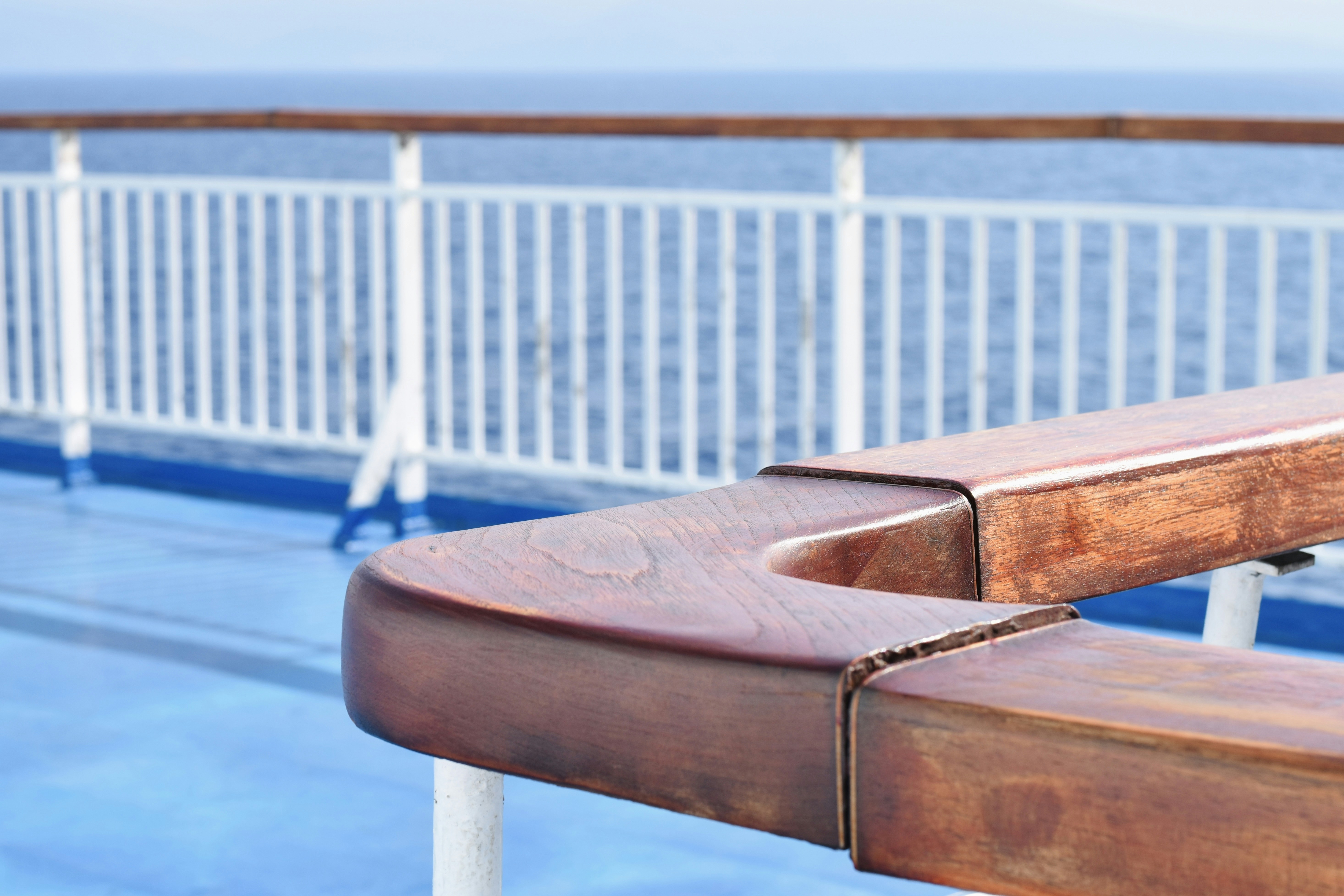 Curved wooden railing at sunlit pool deck with sea horizon