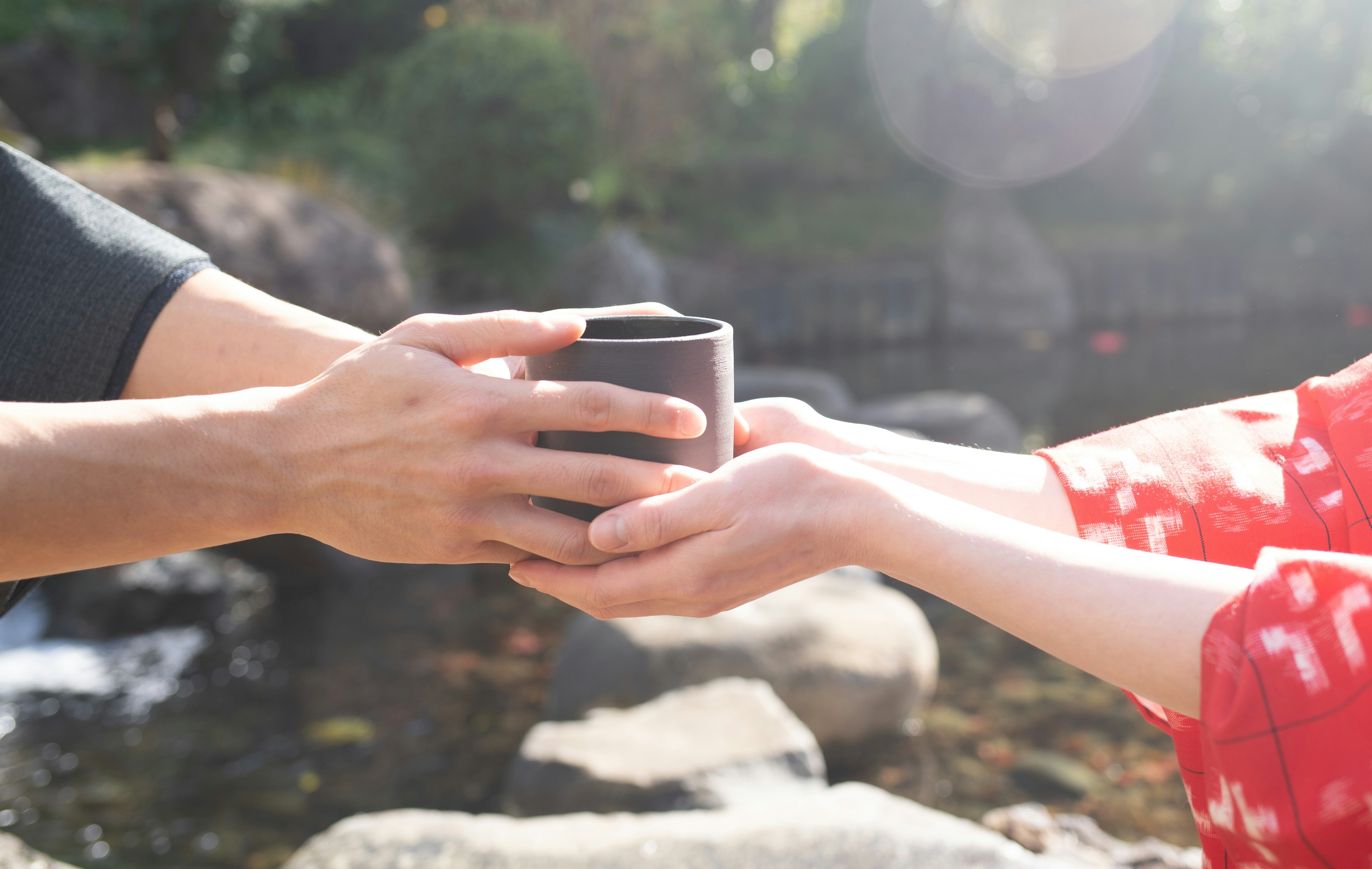 A Shared Toast by the River: Hands Reaching Across a Cup
