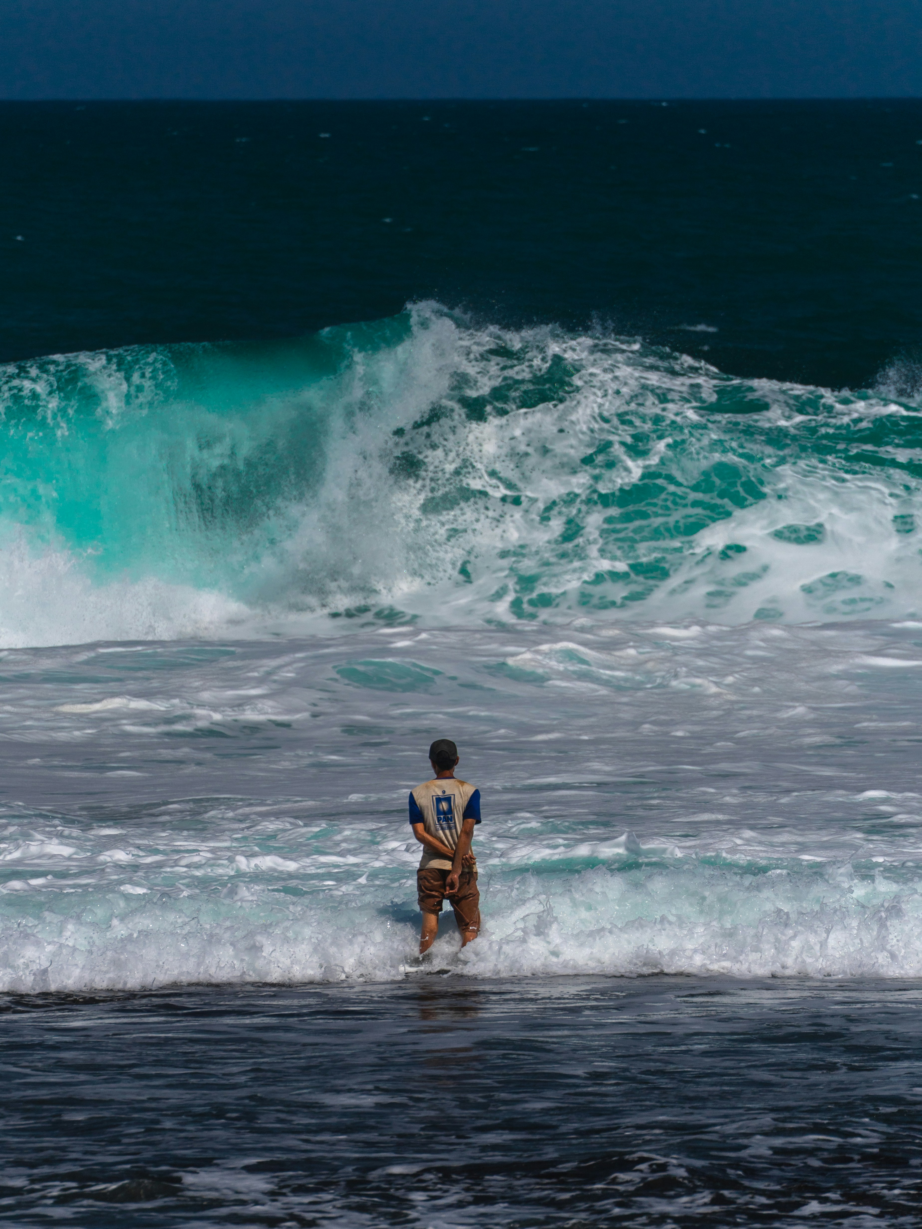  lone beachgoer amid a towering turquoise break at the shore