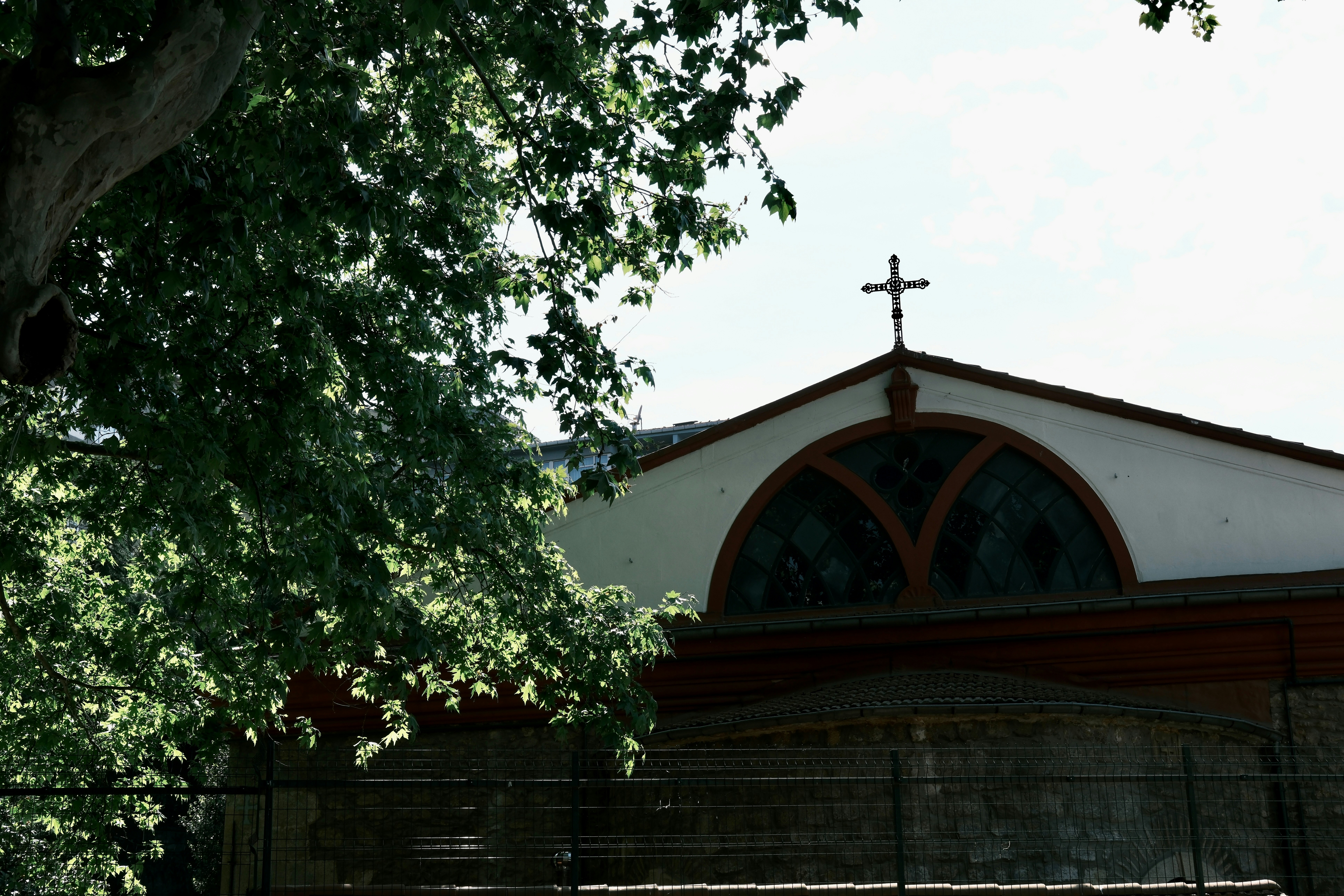 Cross glints above a shaded chapel as tree branches frame the facade
