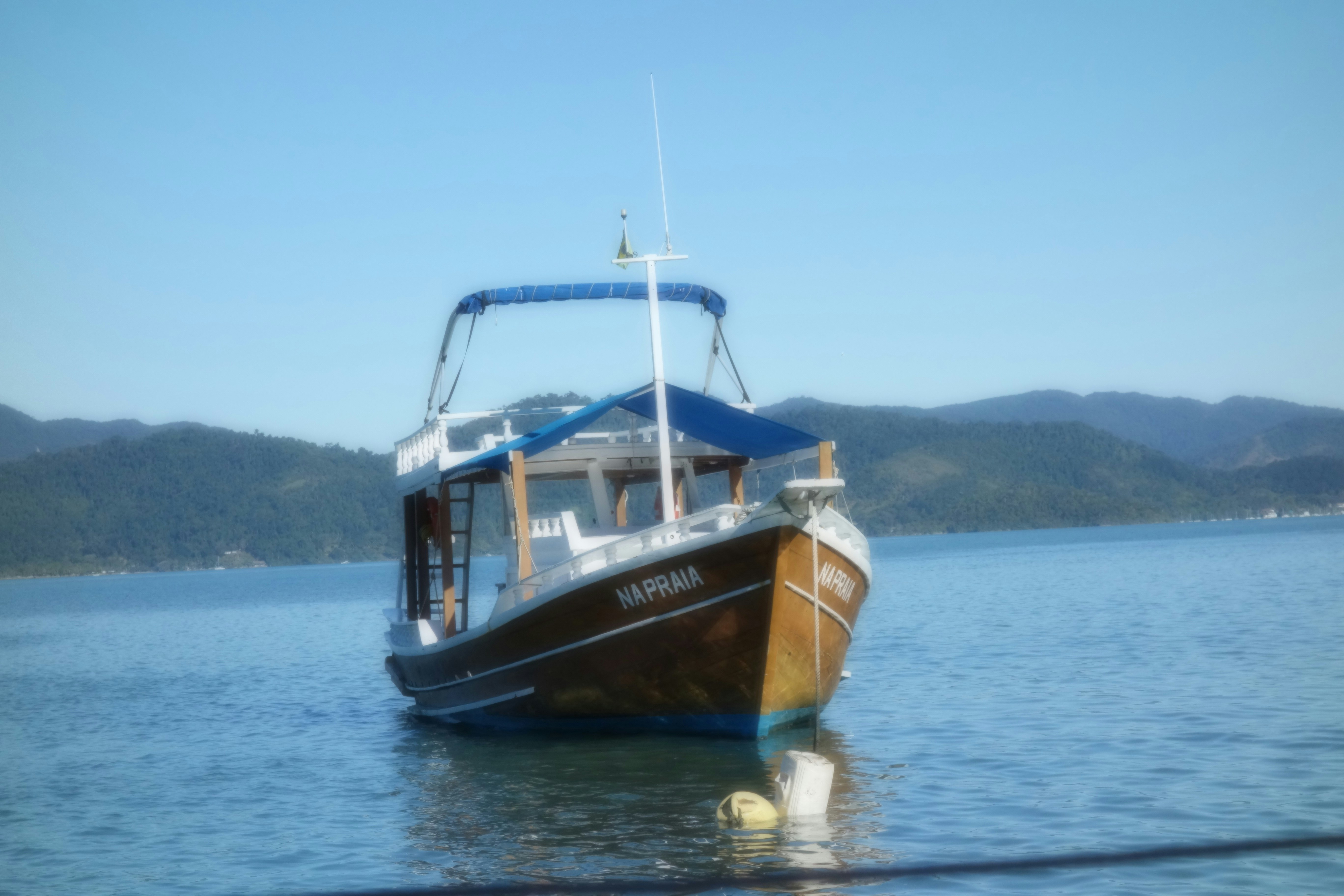 Boat at anchor amid calm blue expanse with distant hills