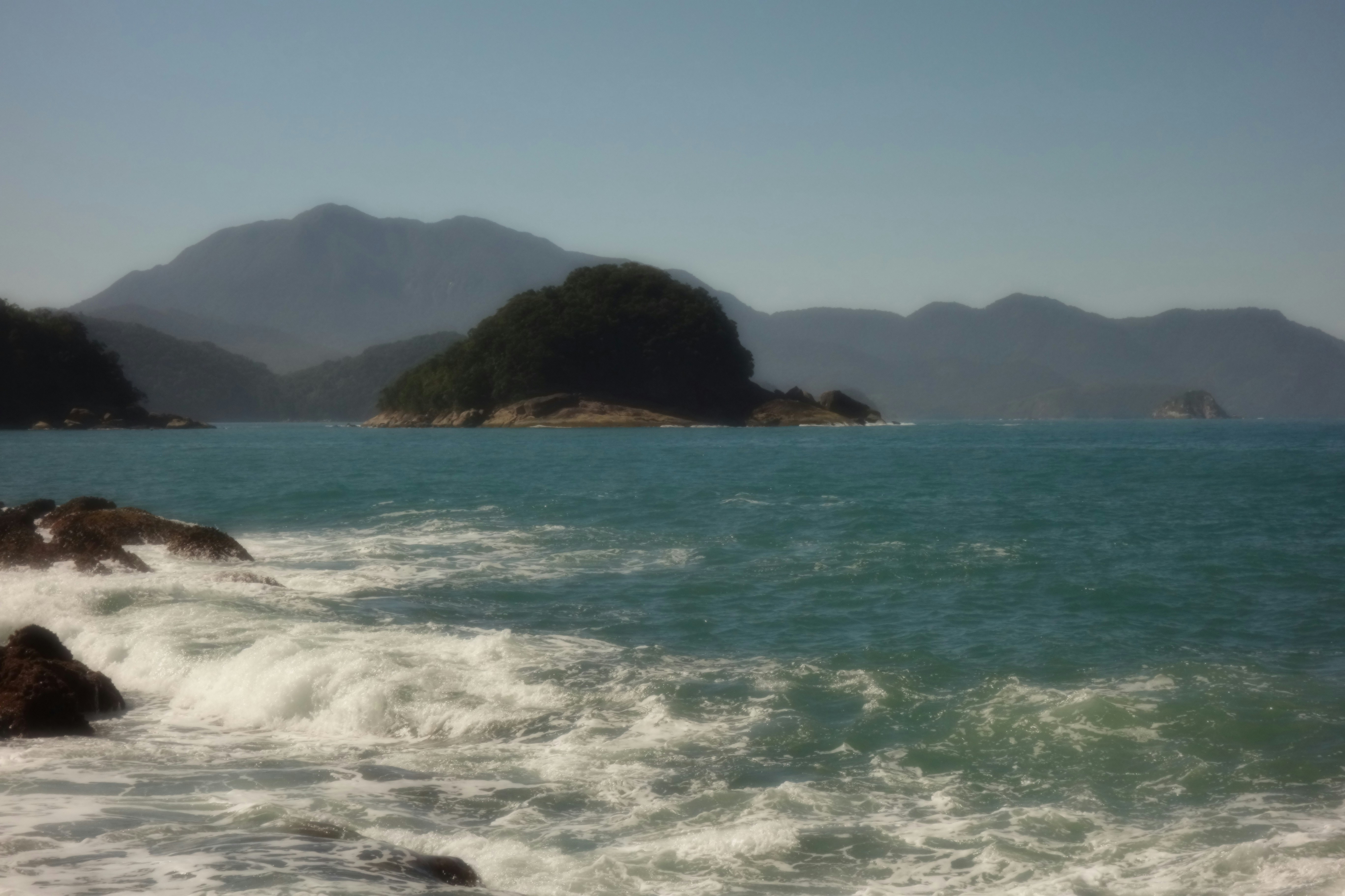 Isolated Island Amid Blue Waves and Distant Mountains