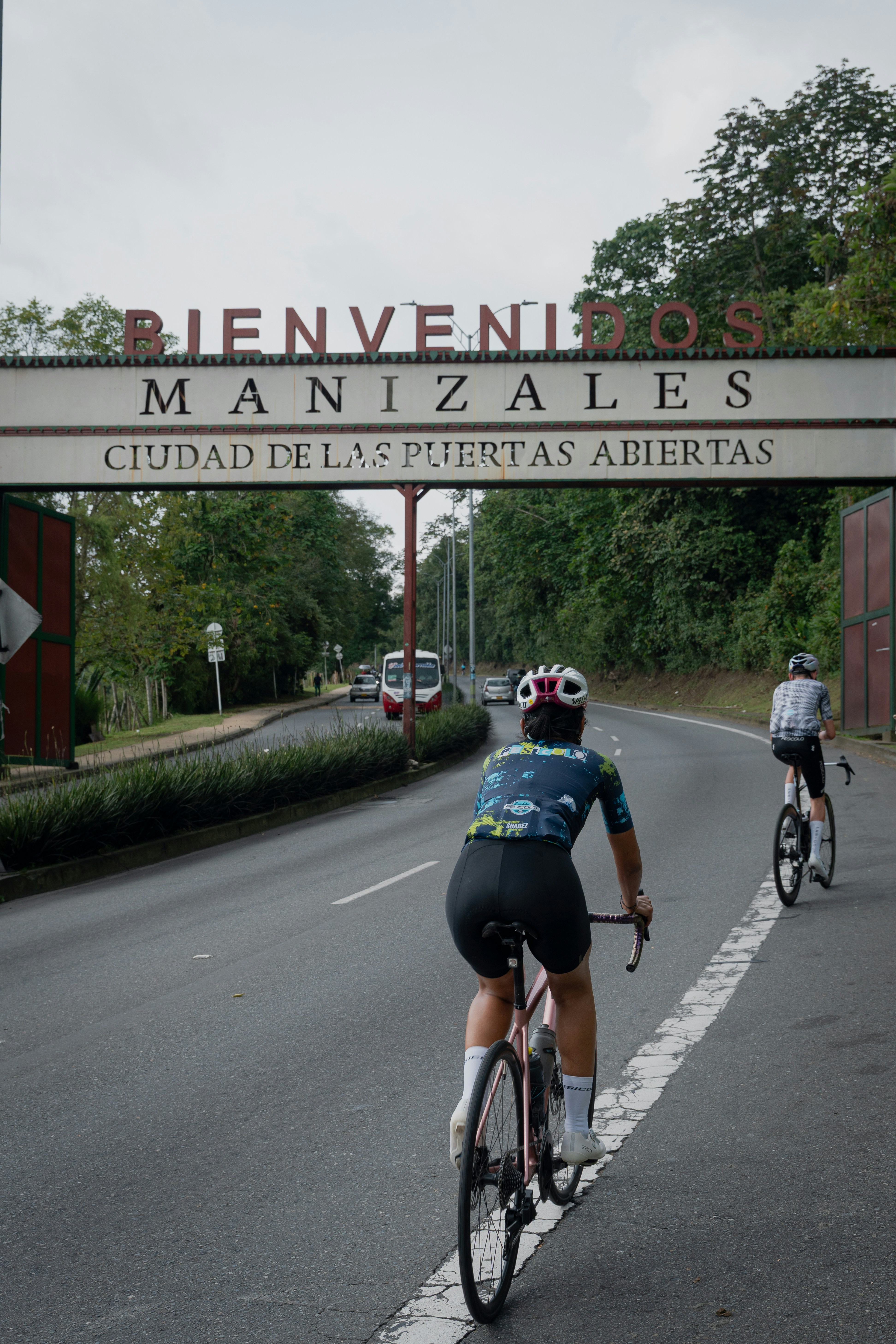 Riders Pedaling Under a Welcome Arch into Manizales