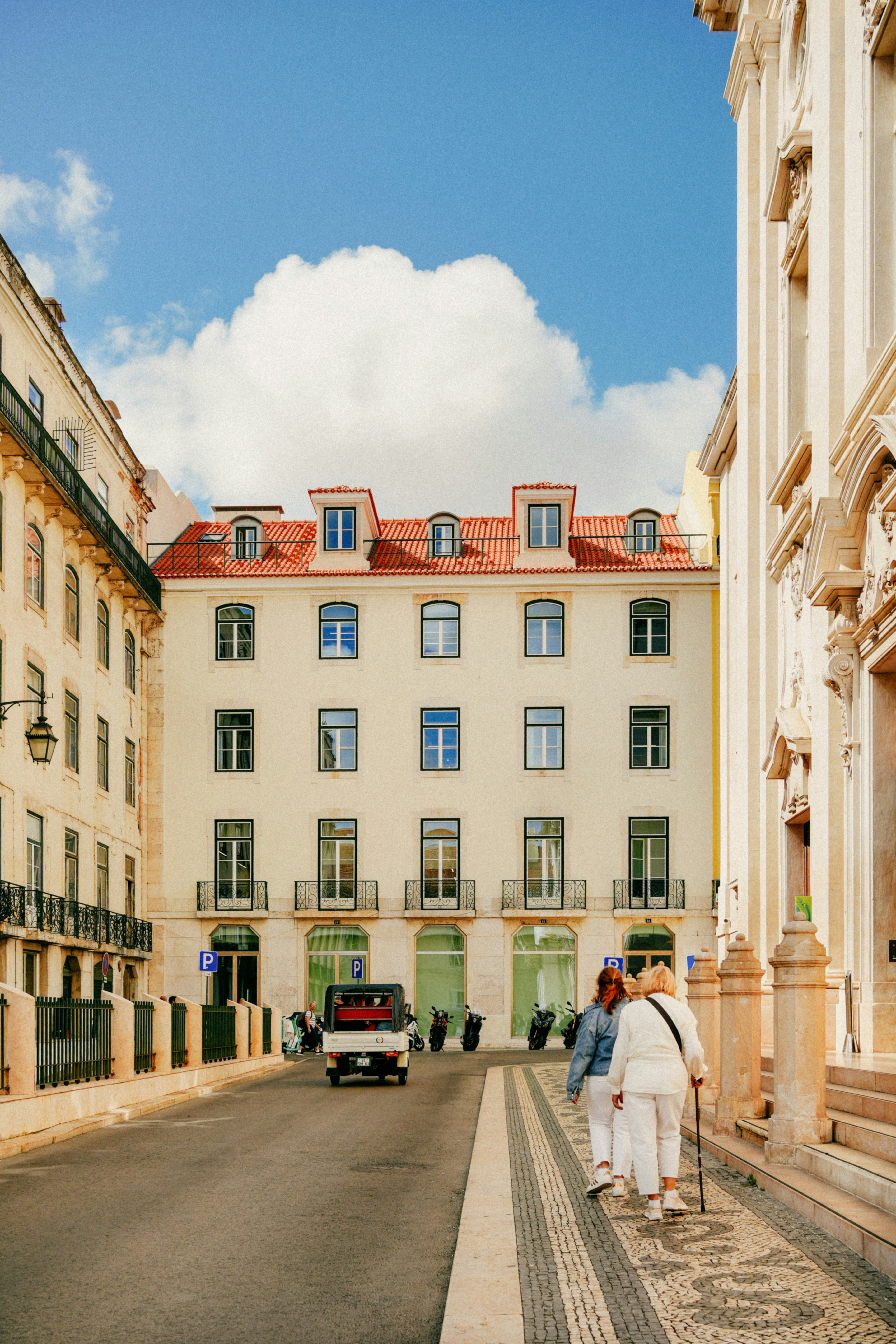 Sunlit European Street: Facades, Shadows, and a Strolling Pair