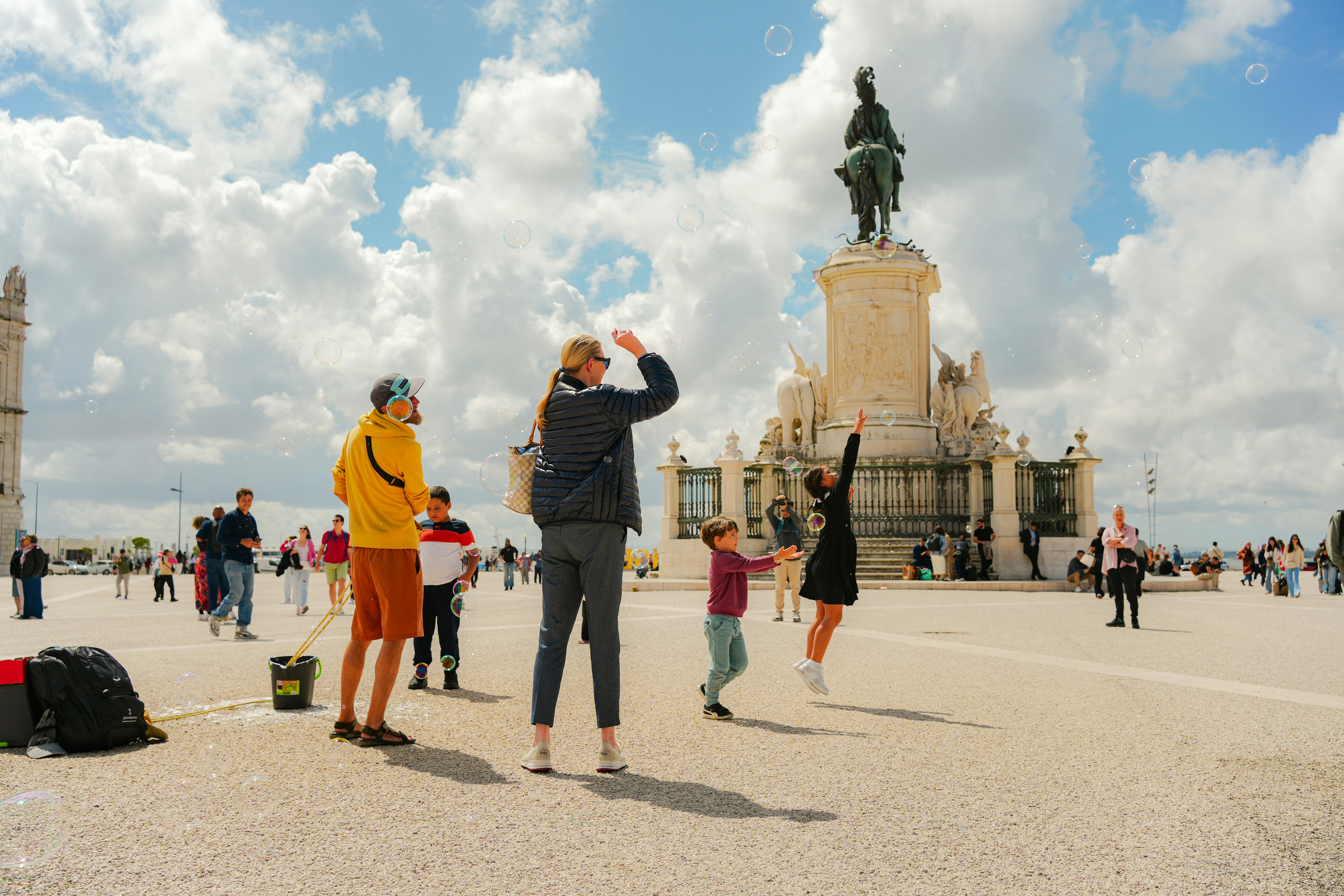 Children’s joyful leap beneath a grand equestrian statue at a sunlit plaza