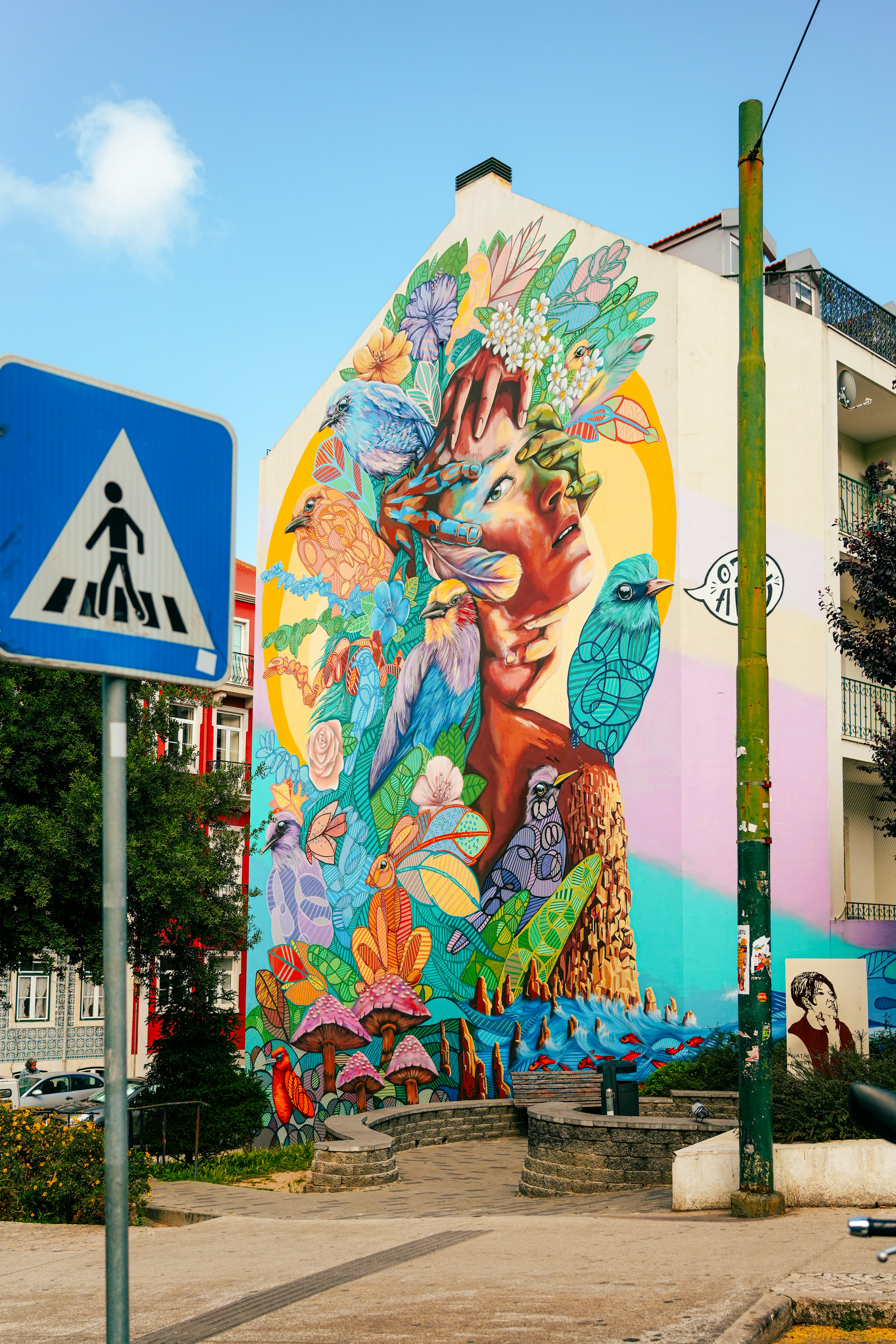 Vibrant mural on a sunlit corner building with pedestrian sign in the foreground
