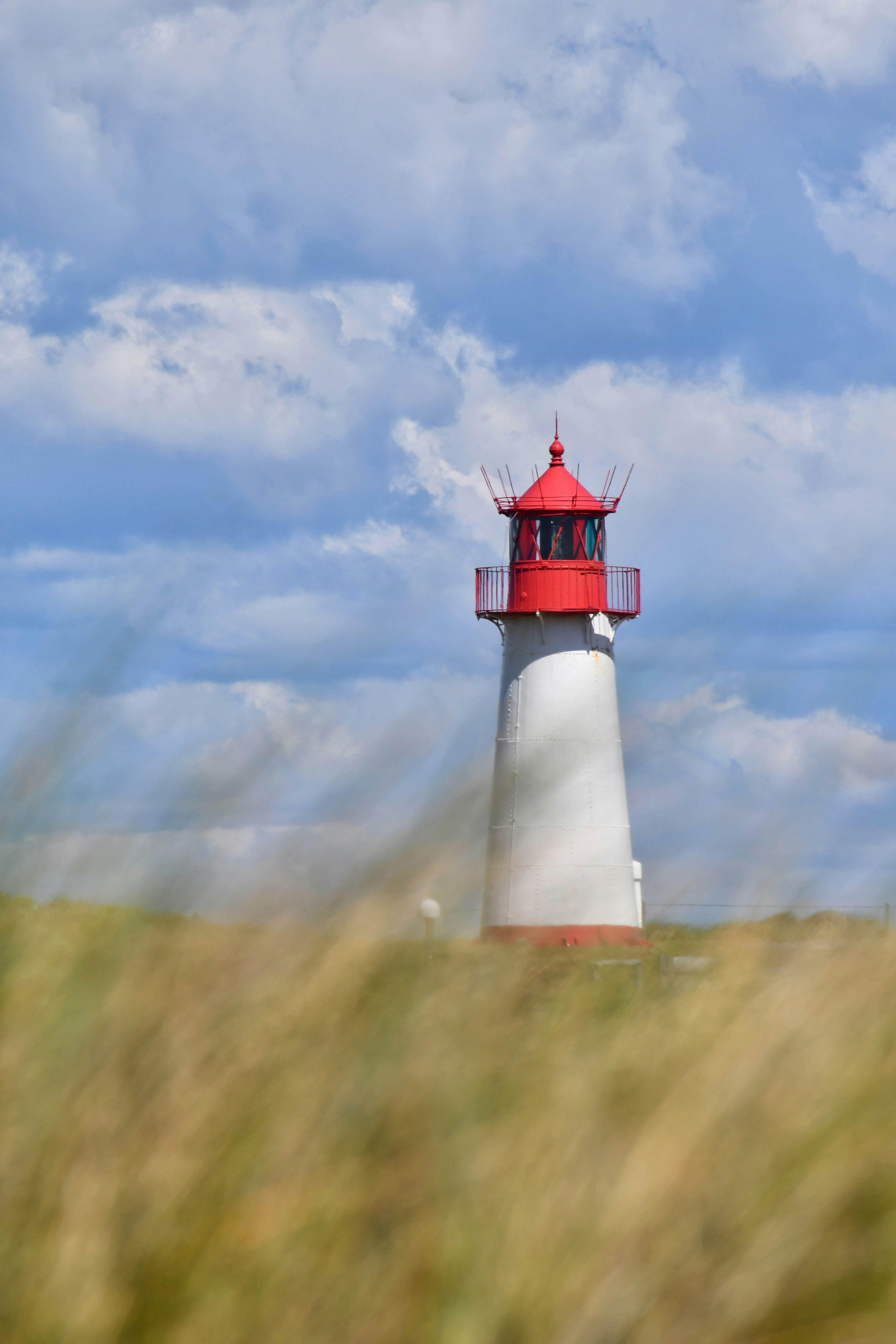 Red Beacon on White: A Lone Lighthouse Against a Sky of Clouds