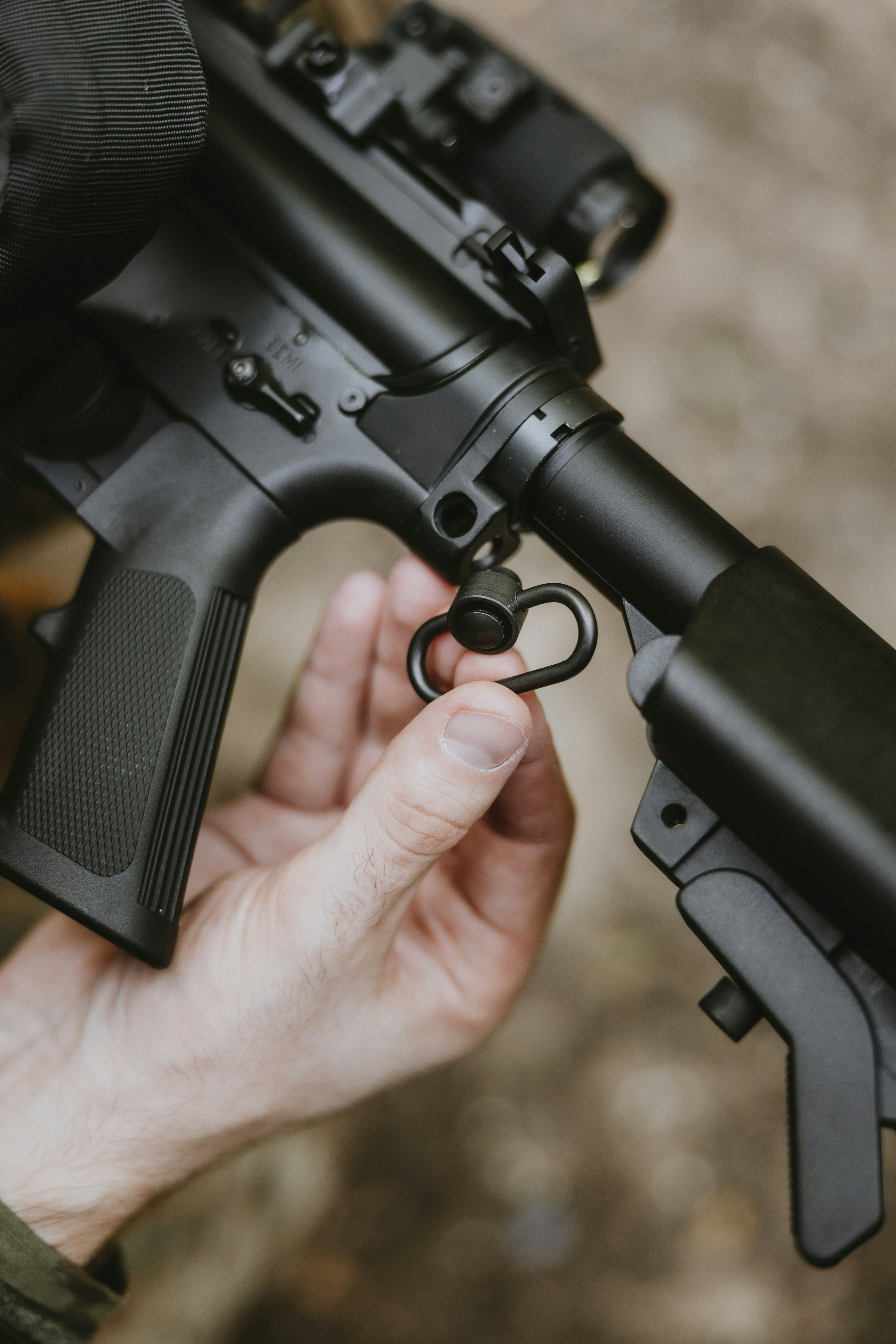 Close-up of a person adjusting the pistol's quick-detach sling ring on a rifle, showing fingers and the receiver in soft focus. (Logo-free, still image.)