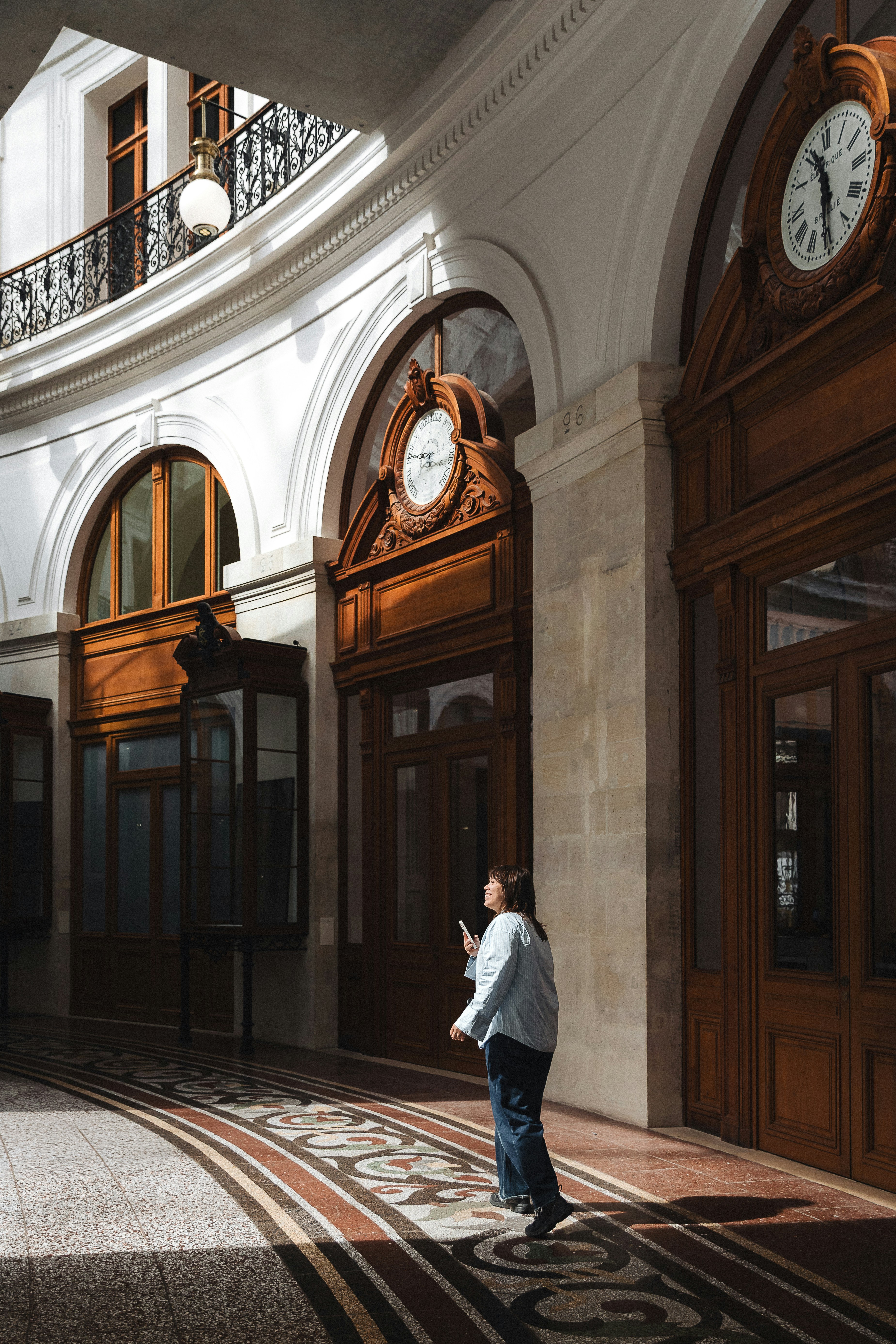Man walks through a sunlit grand arcade with ornate clocks