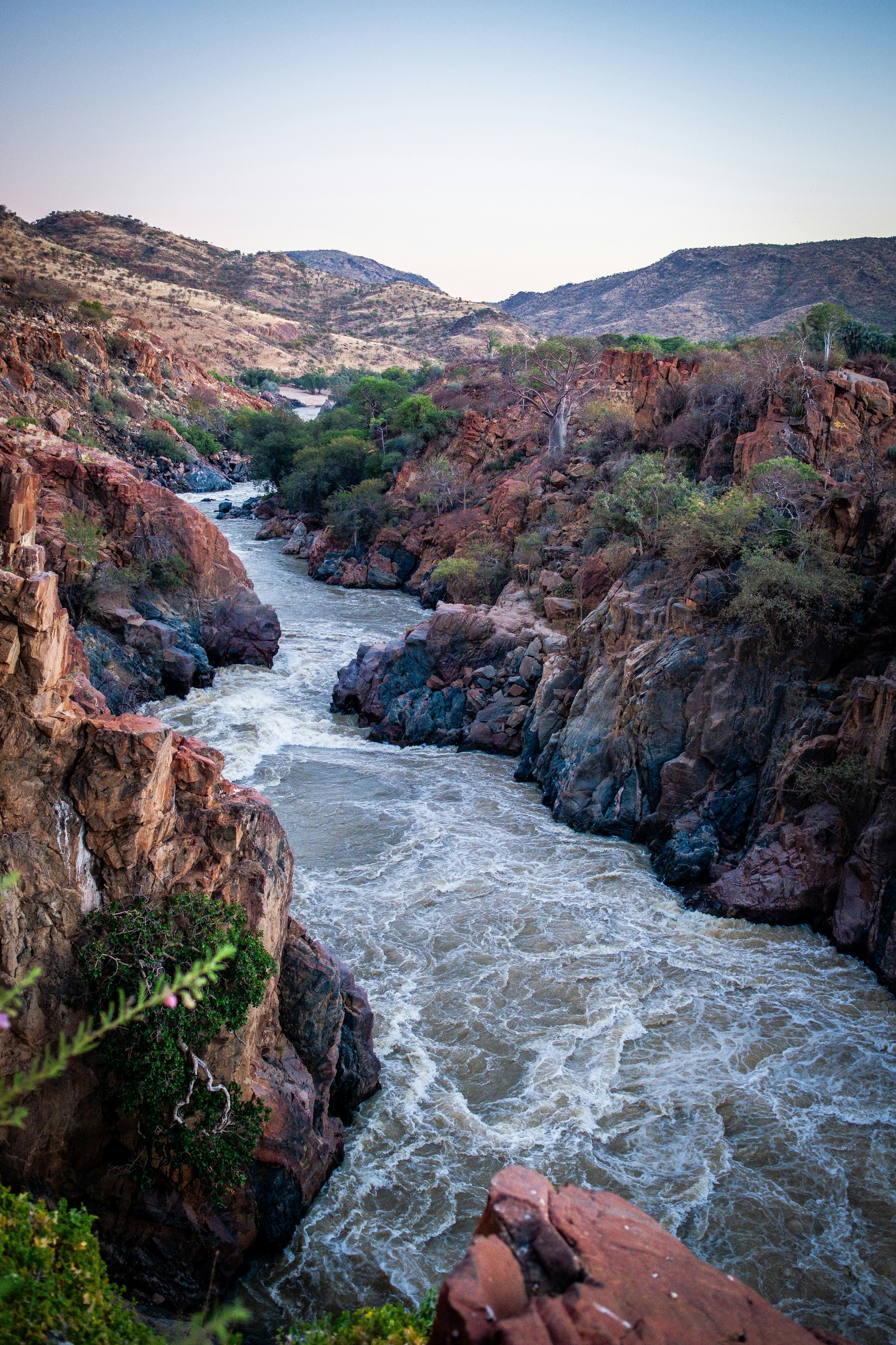 Rugged Gorge Rush: River Winding Between Red Cliff and Green Foliage