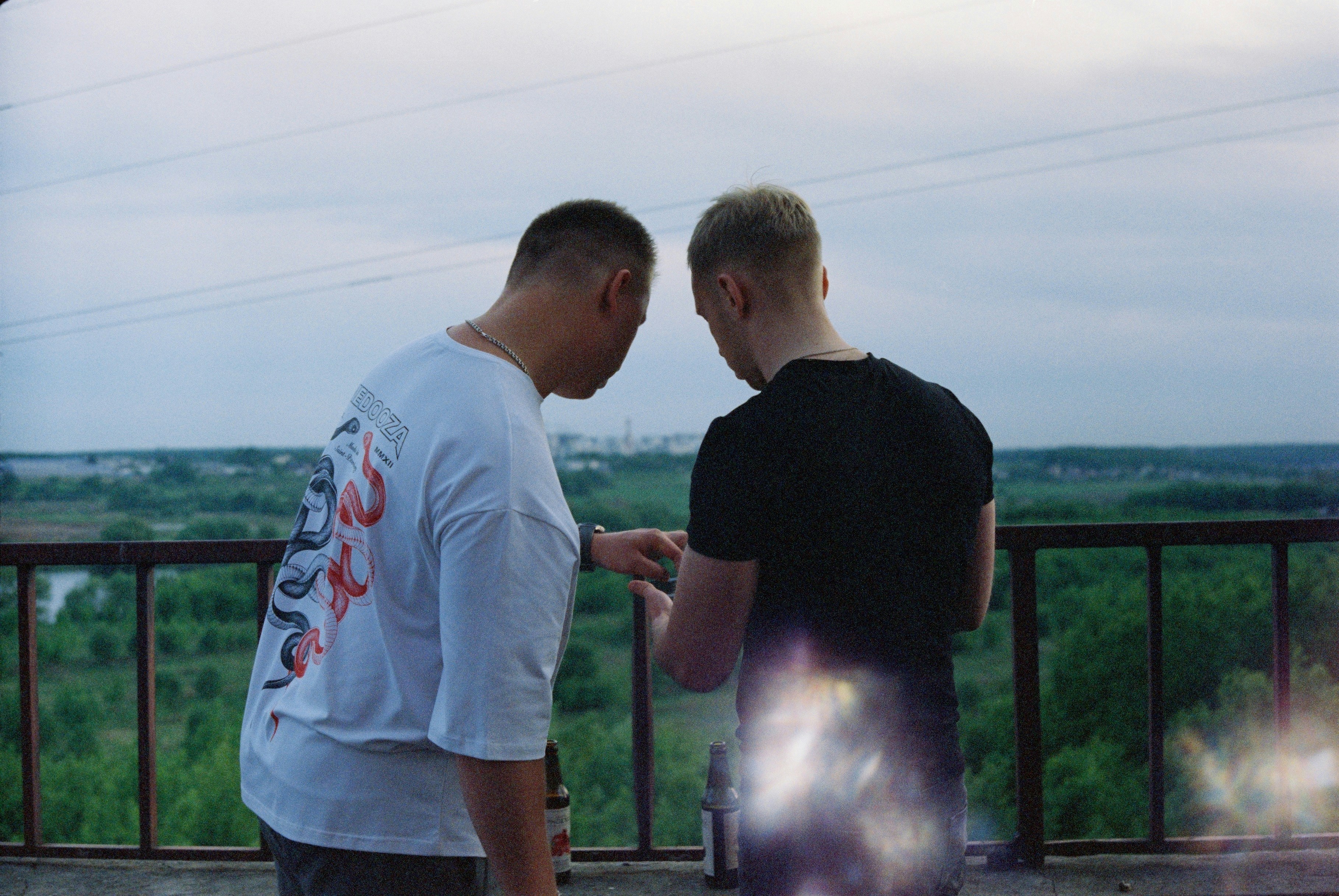 Two friends on a rooftop overlooking a green valley at dusk