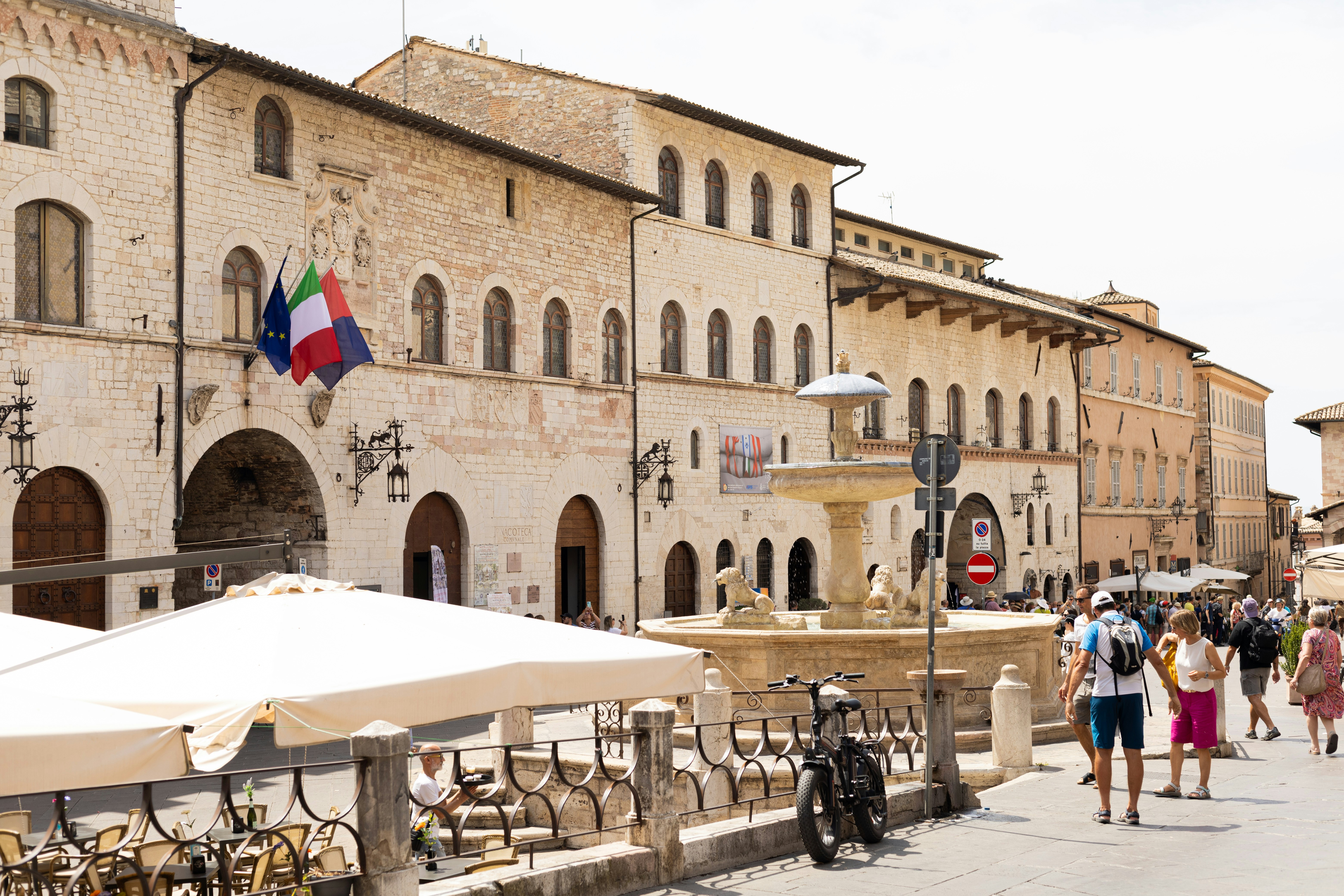 Sunlit Piazza Corridor: Flags, Fountains, and Footpath Buzz