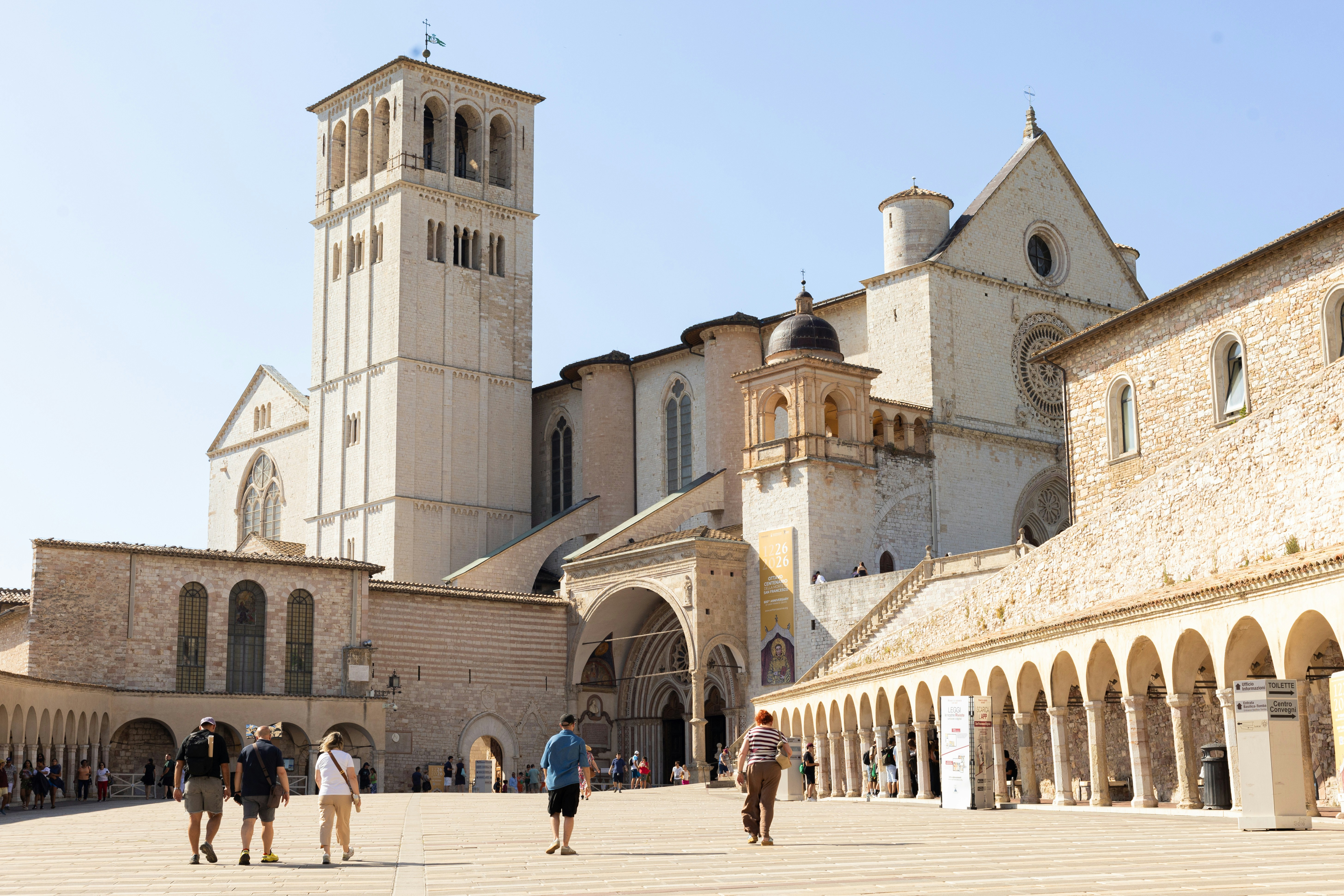 People walk in a large courtyard before an ancient basilica.