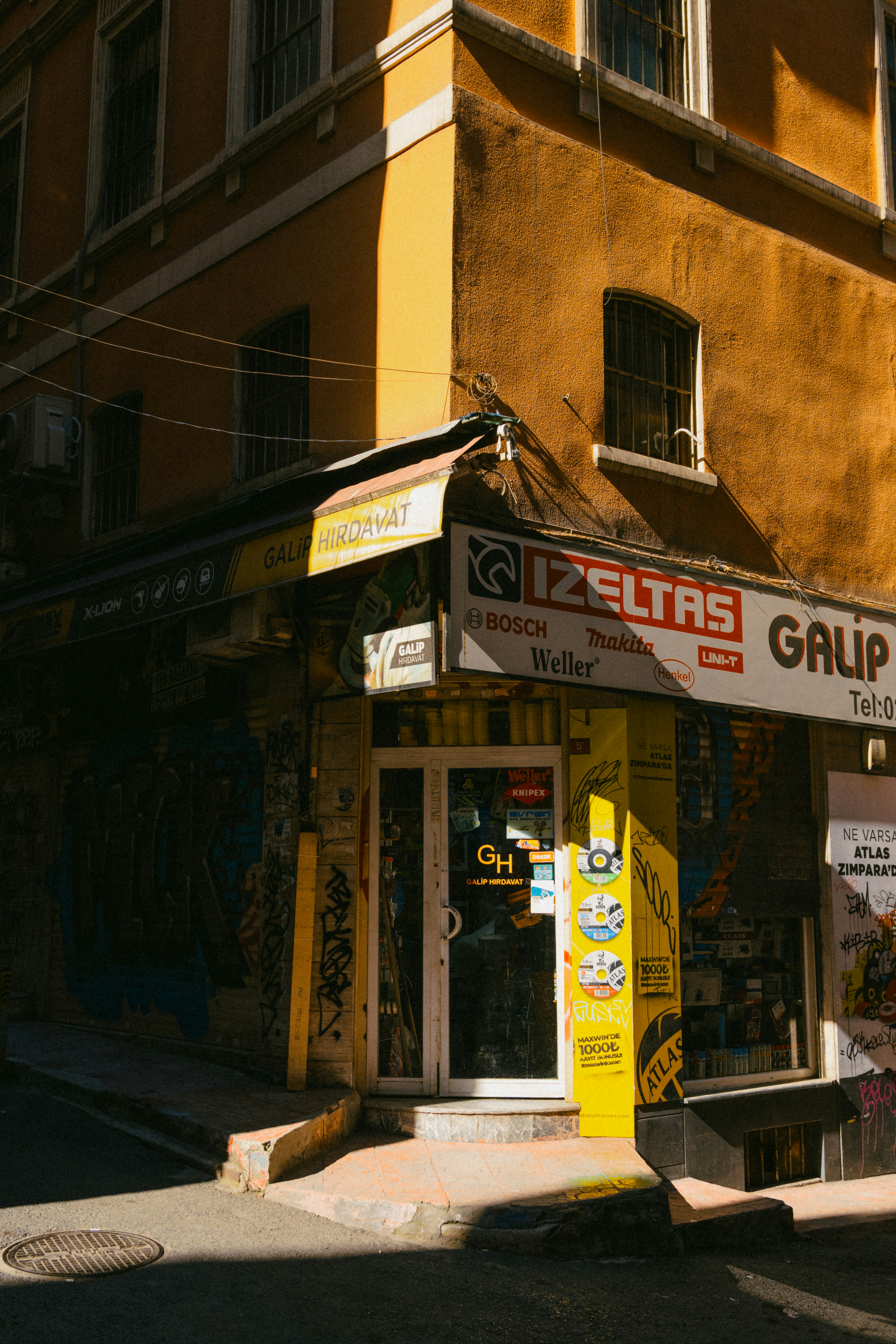 Sunlit yellow building with a corner shop and street art.
