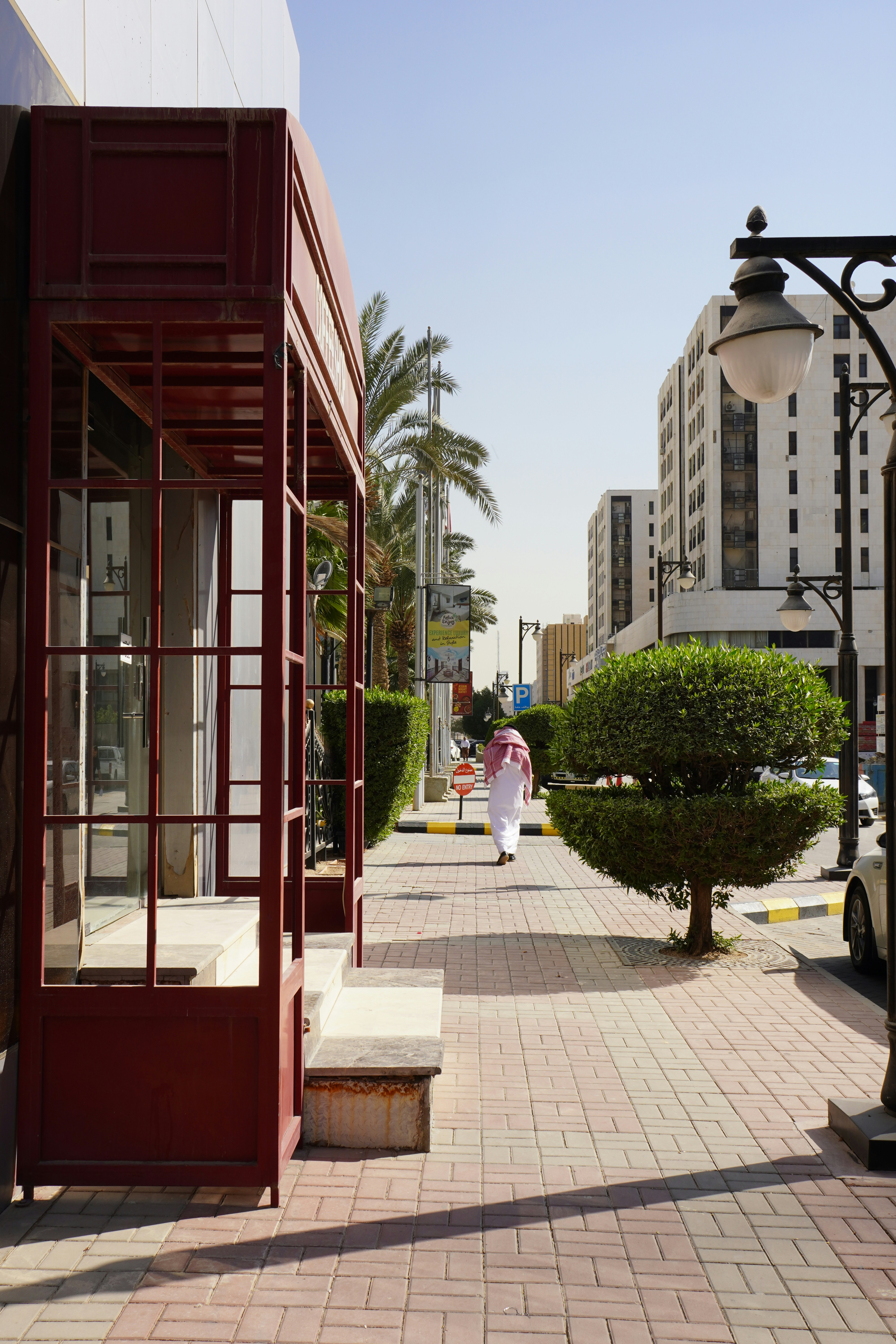Street-Front Geometry: Red Canopy, Palm Shadows, and Quiet Walk