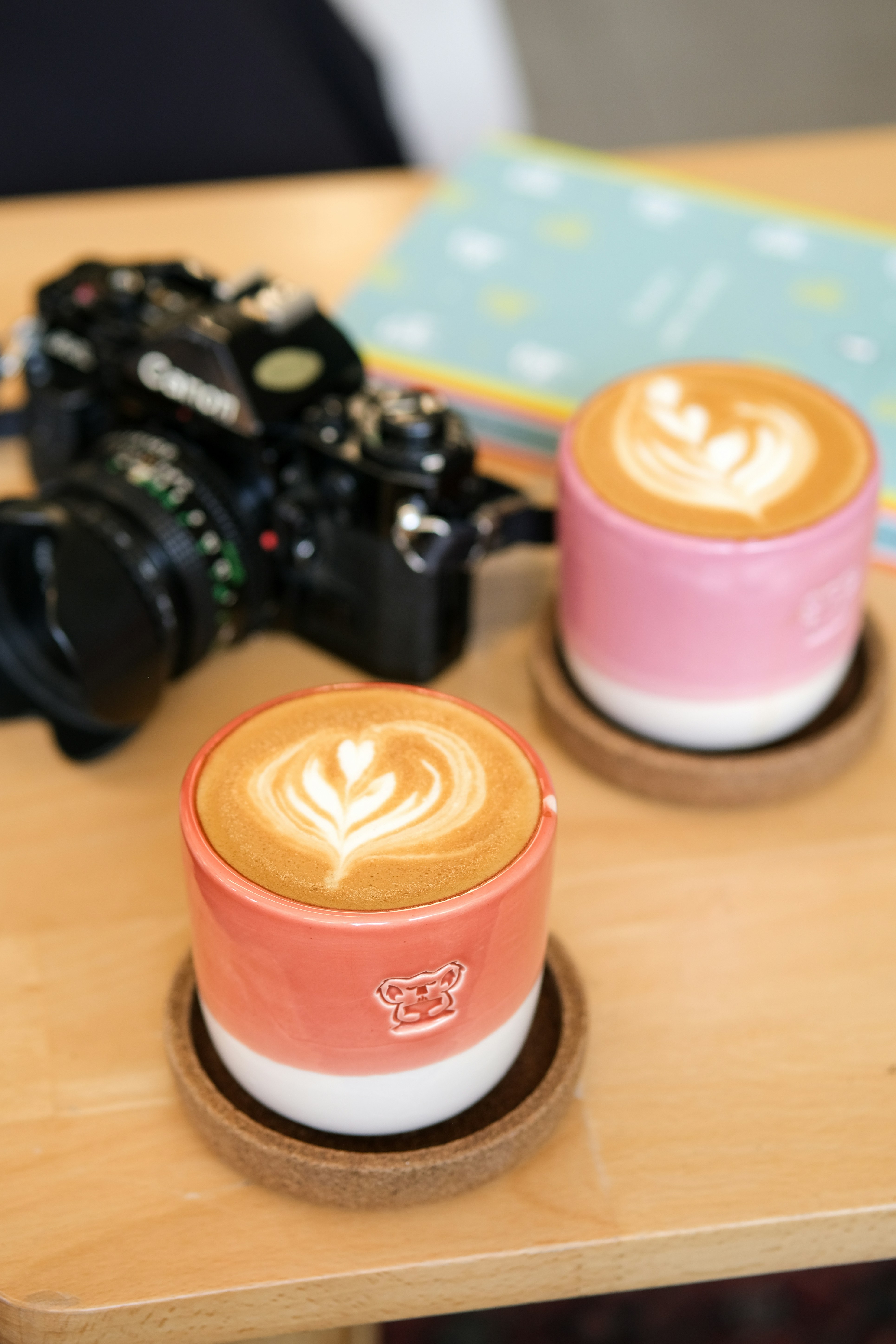 Coffee Art and Camera Glow: Two Latte Hearts Foreground the Vintage Lens