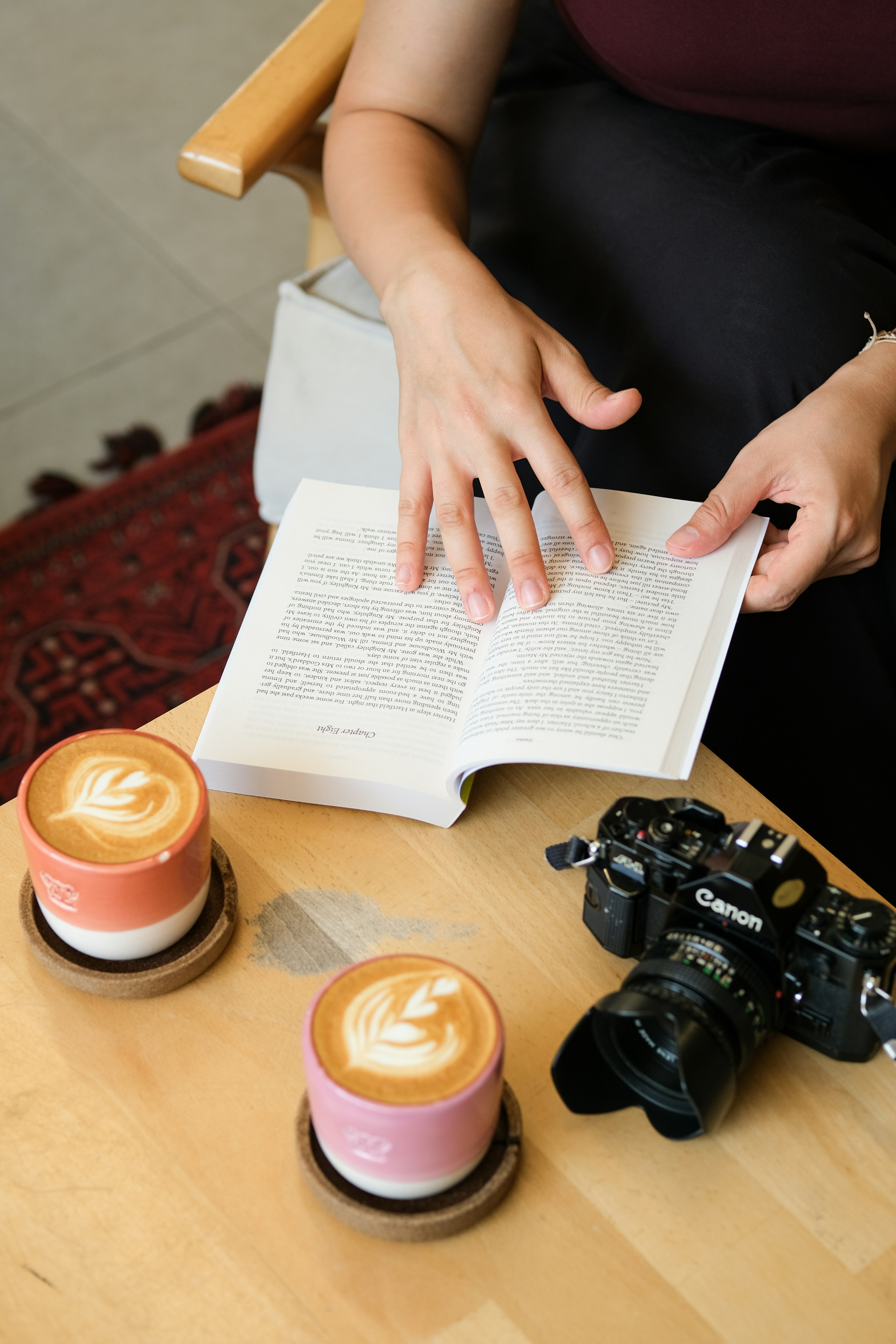 Hands in a Book: Quiet Moment Among Coffee and Camera Gear