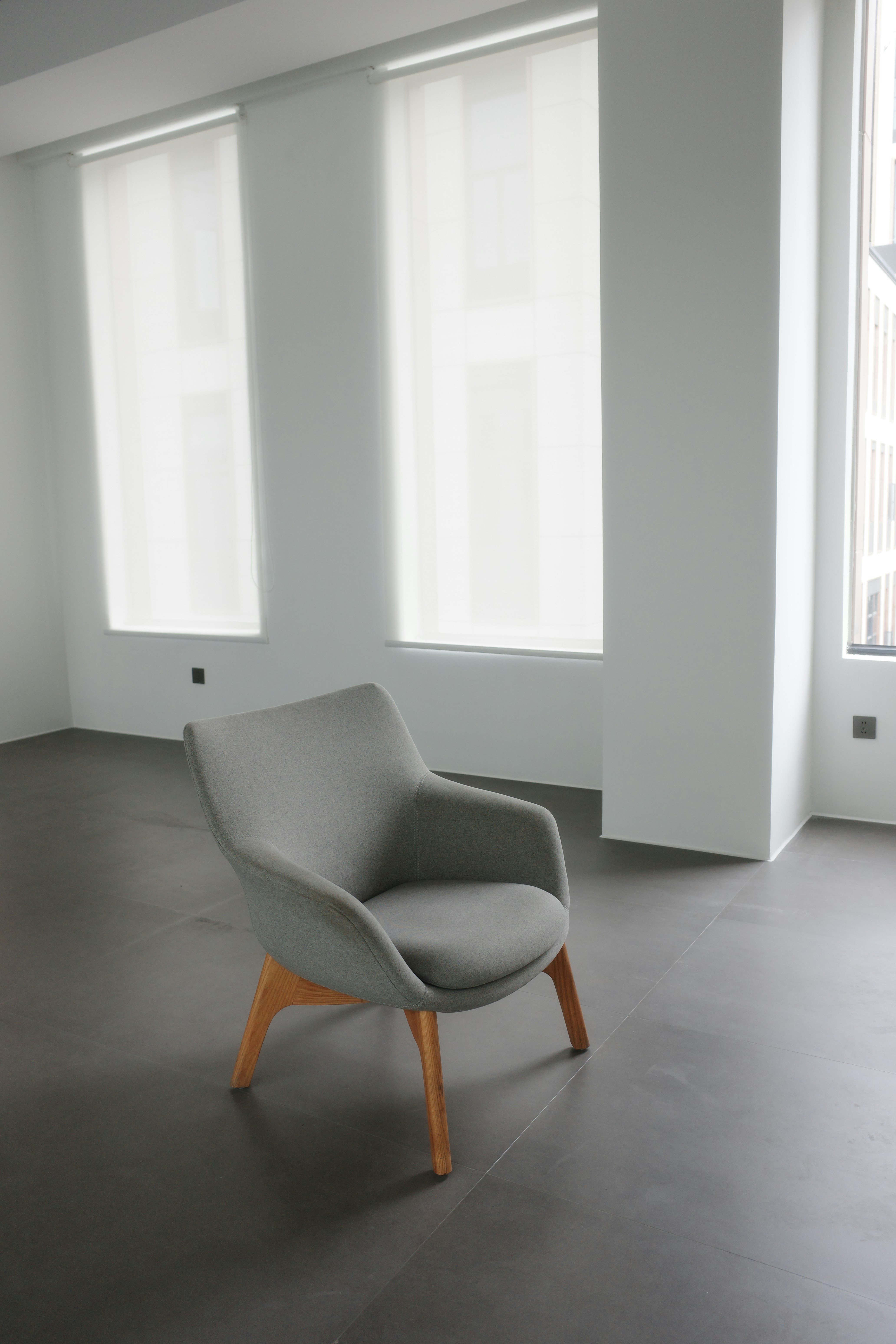 A grey armchair with wooden legs in a minimalist room.