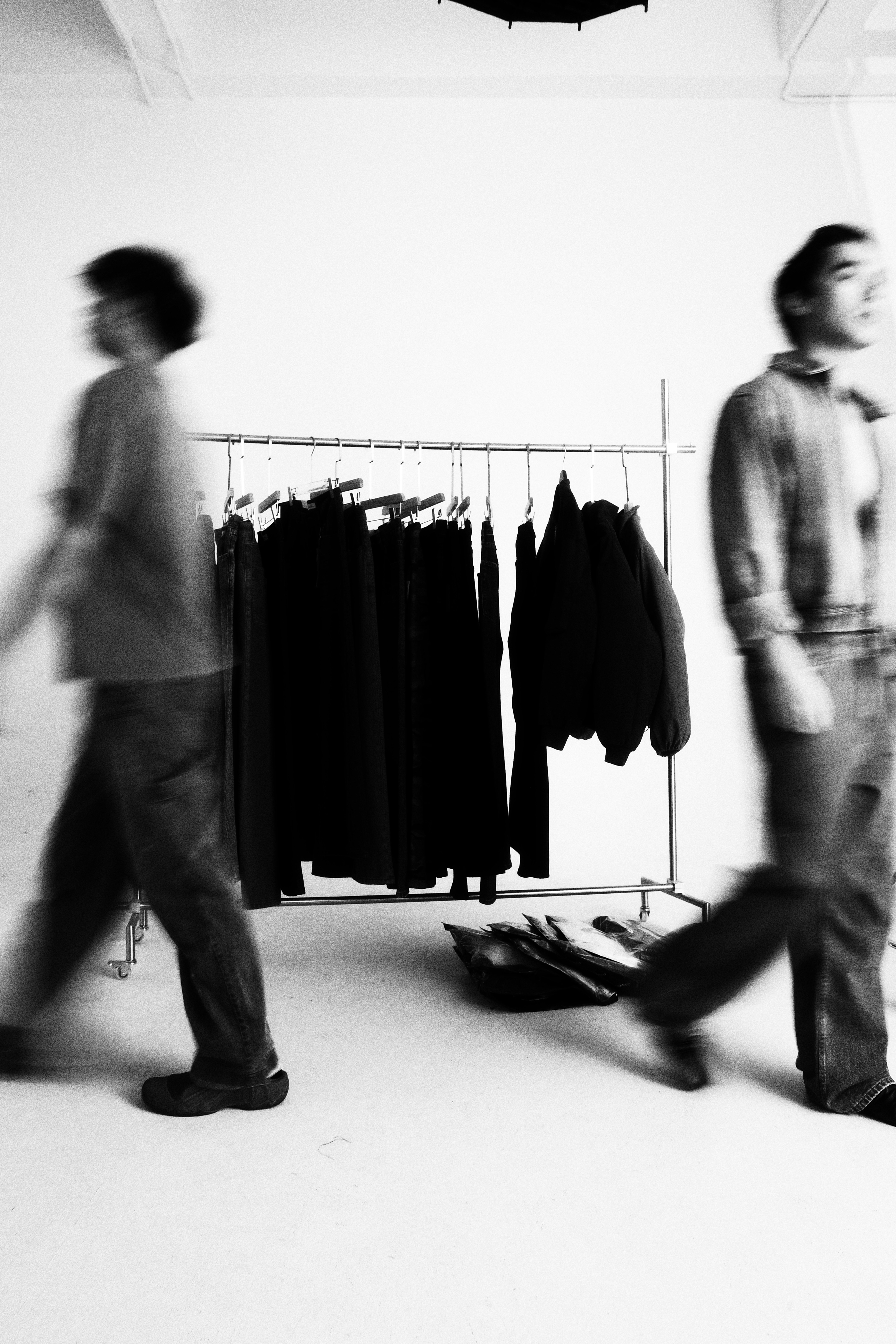 Motion-blurred people walk past a clothing rack.