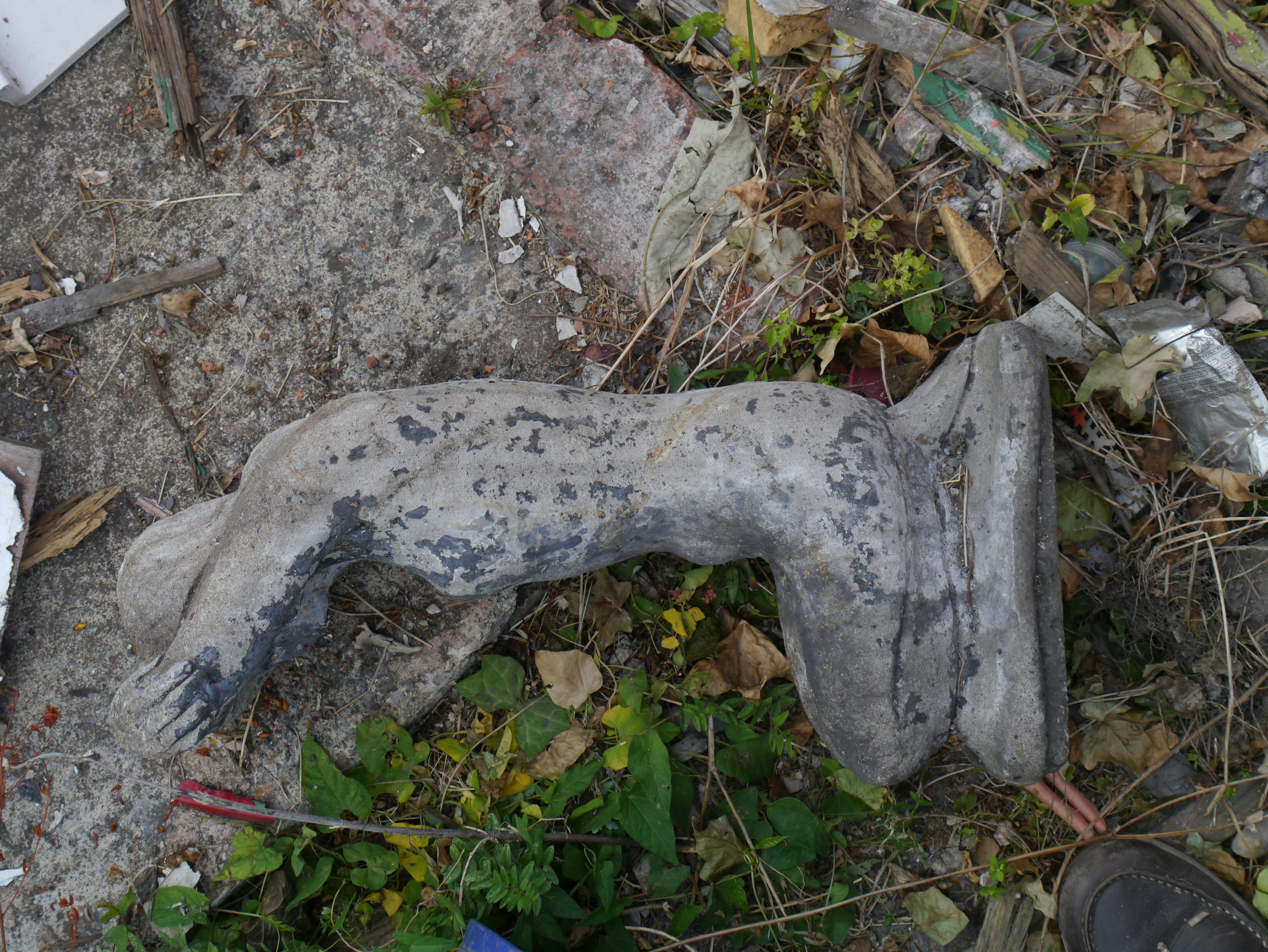 Weathered sculpture fragment resting among debris and foliage