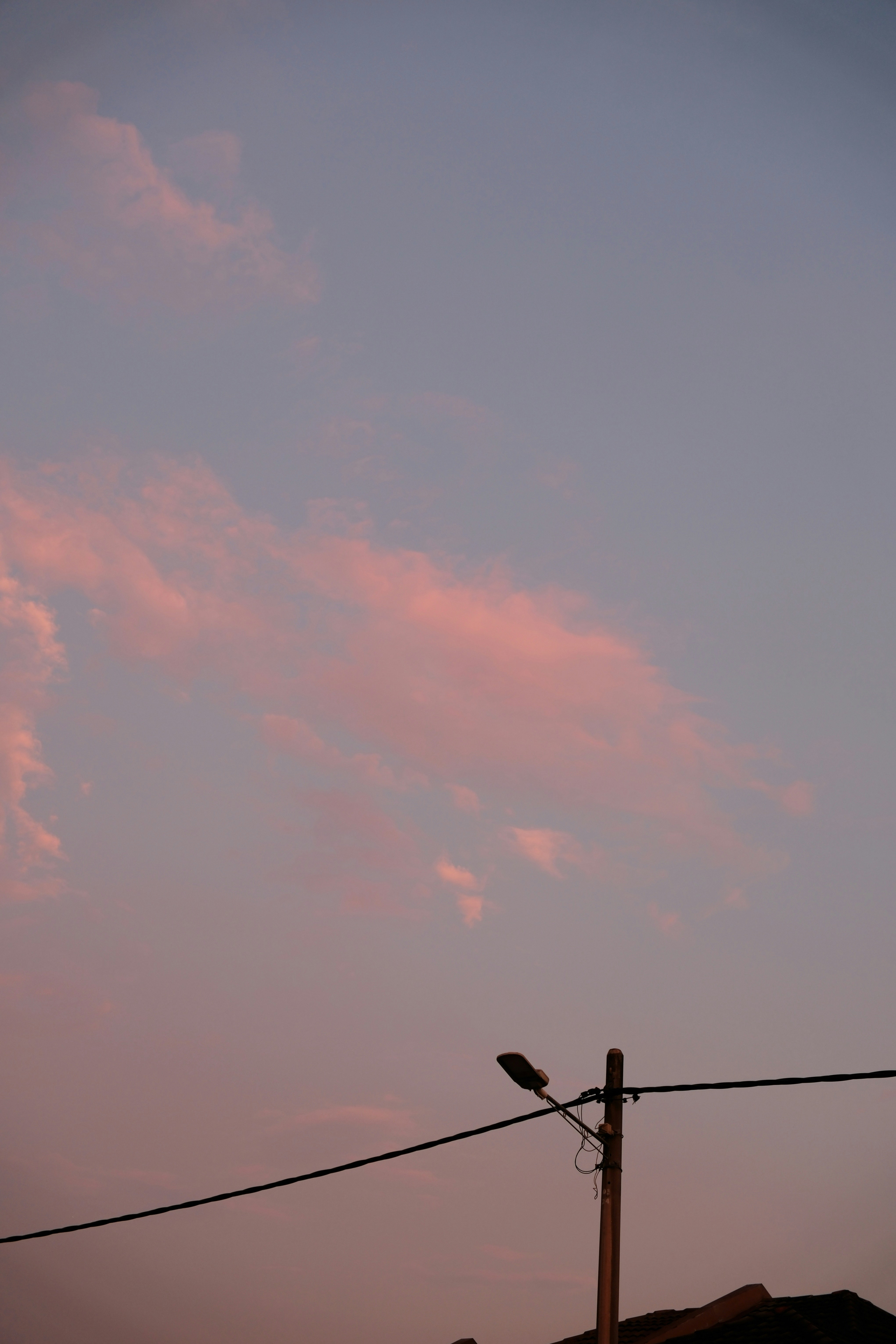 Soft pink clouds drift above a lone utility pole and wires silhouetted against a pastel sky.
