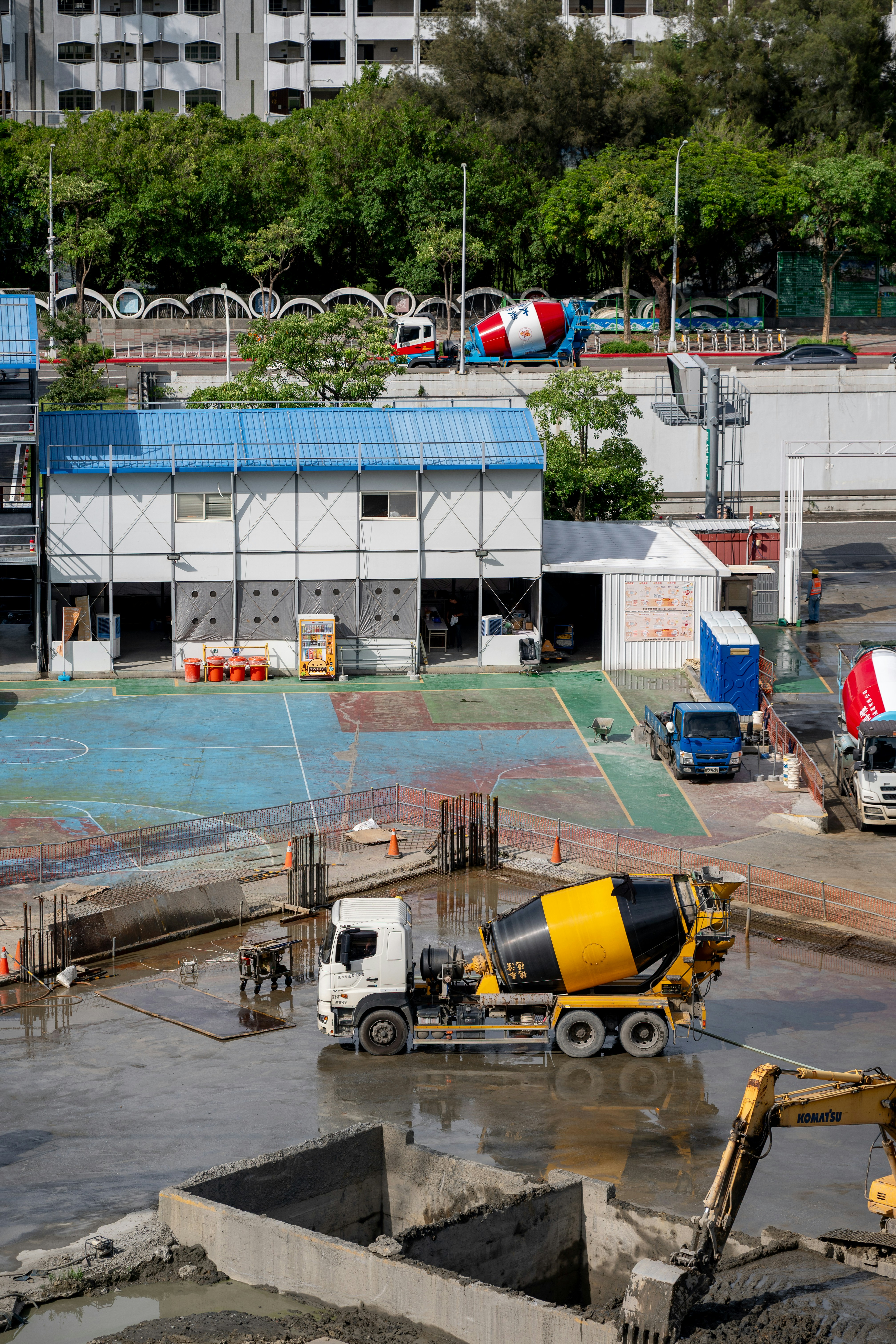 Concrete Playground: A Worksite Tableau with a Bright Cement Mixer Amid Waiting Vehicles