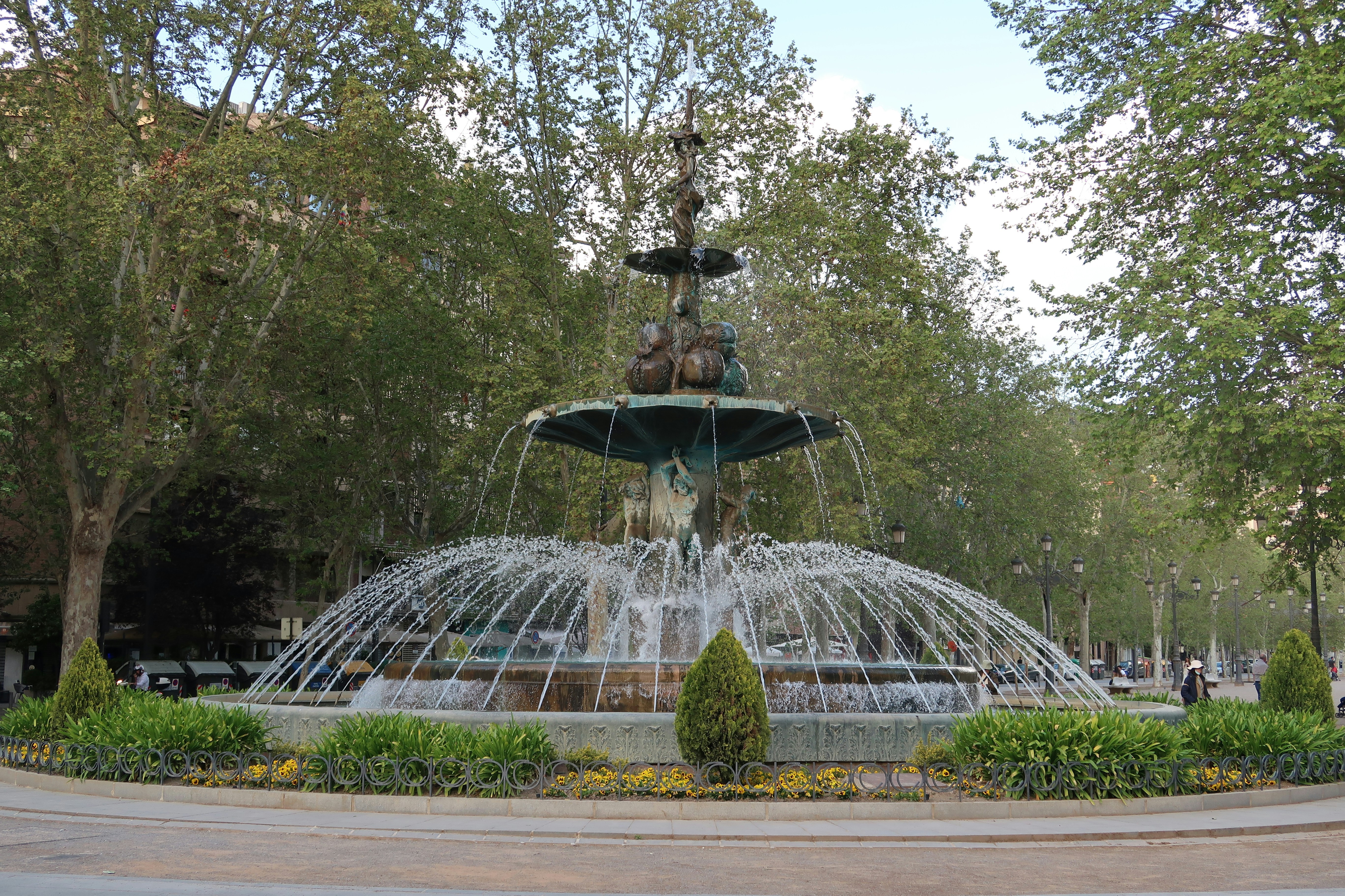 A tiered fountain centerpiece framed by leafy trees in a city plaza