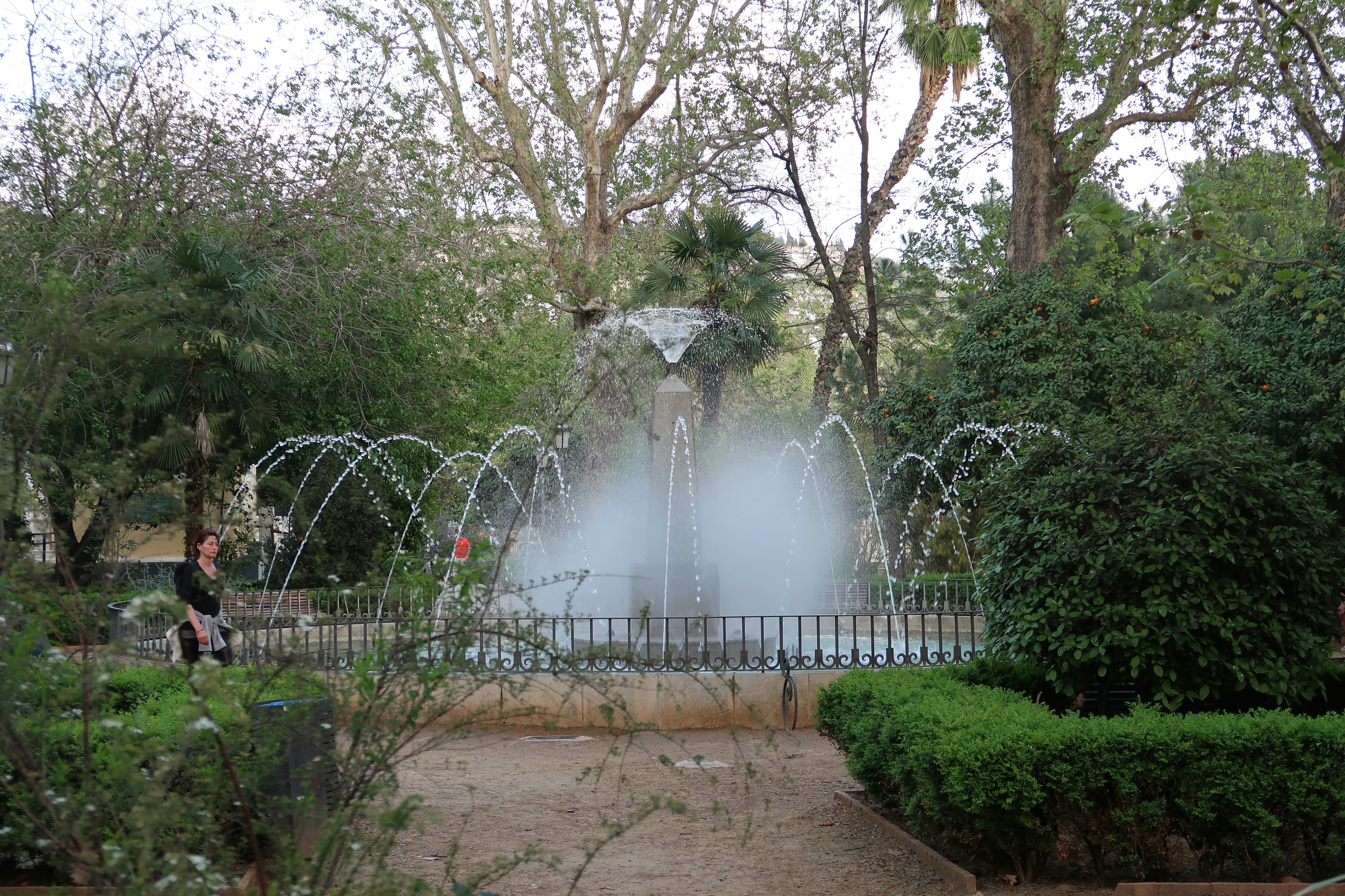 A Quiet Fountain Arc: Garden Visitors Beside Arching Water