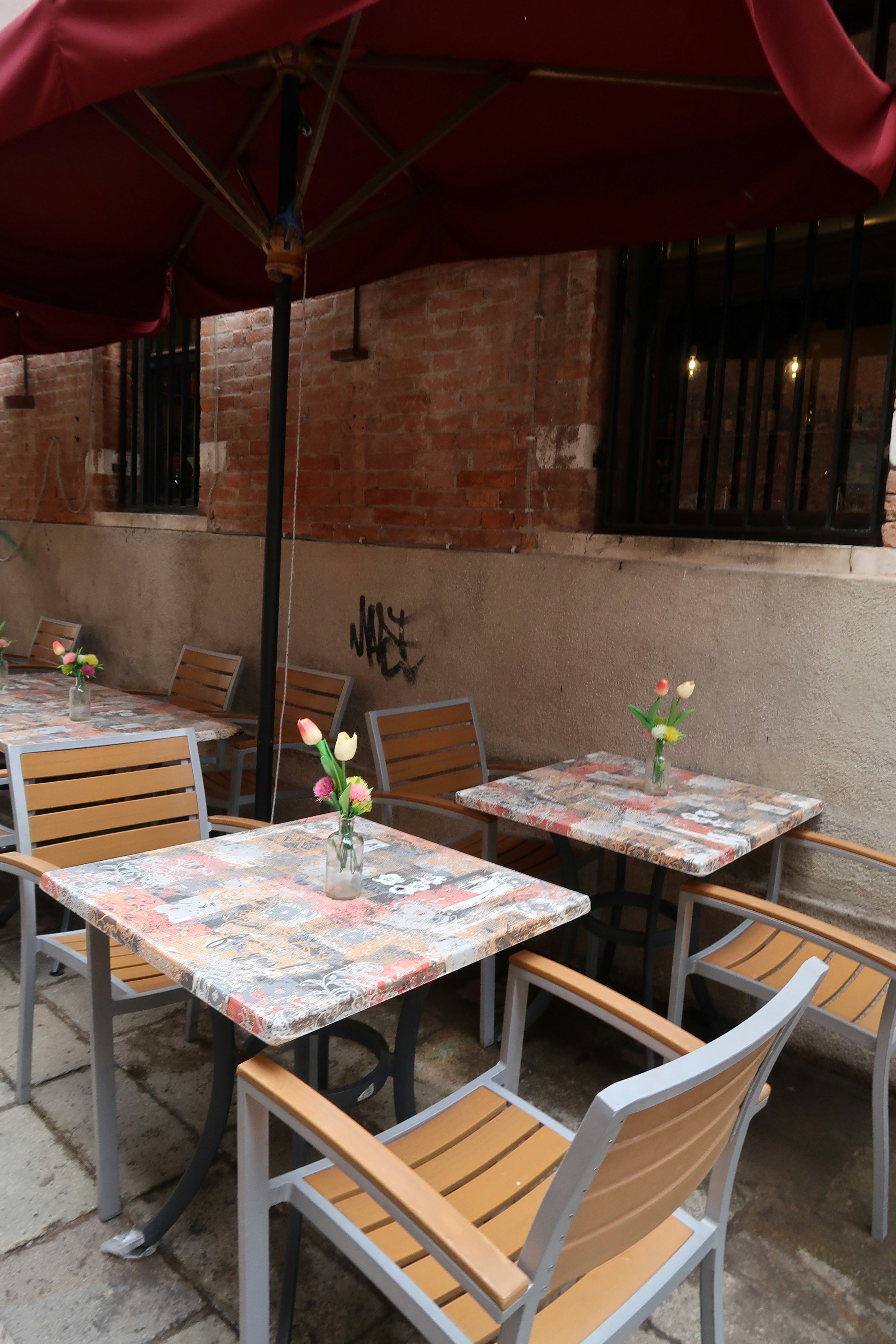 Cobblestone Café Terrace with Floral Arrangements under a Red Canopy