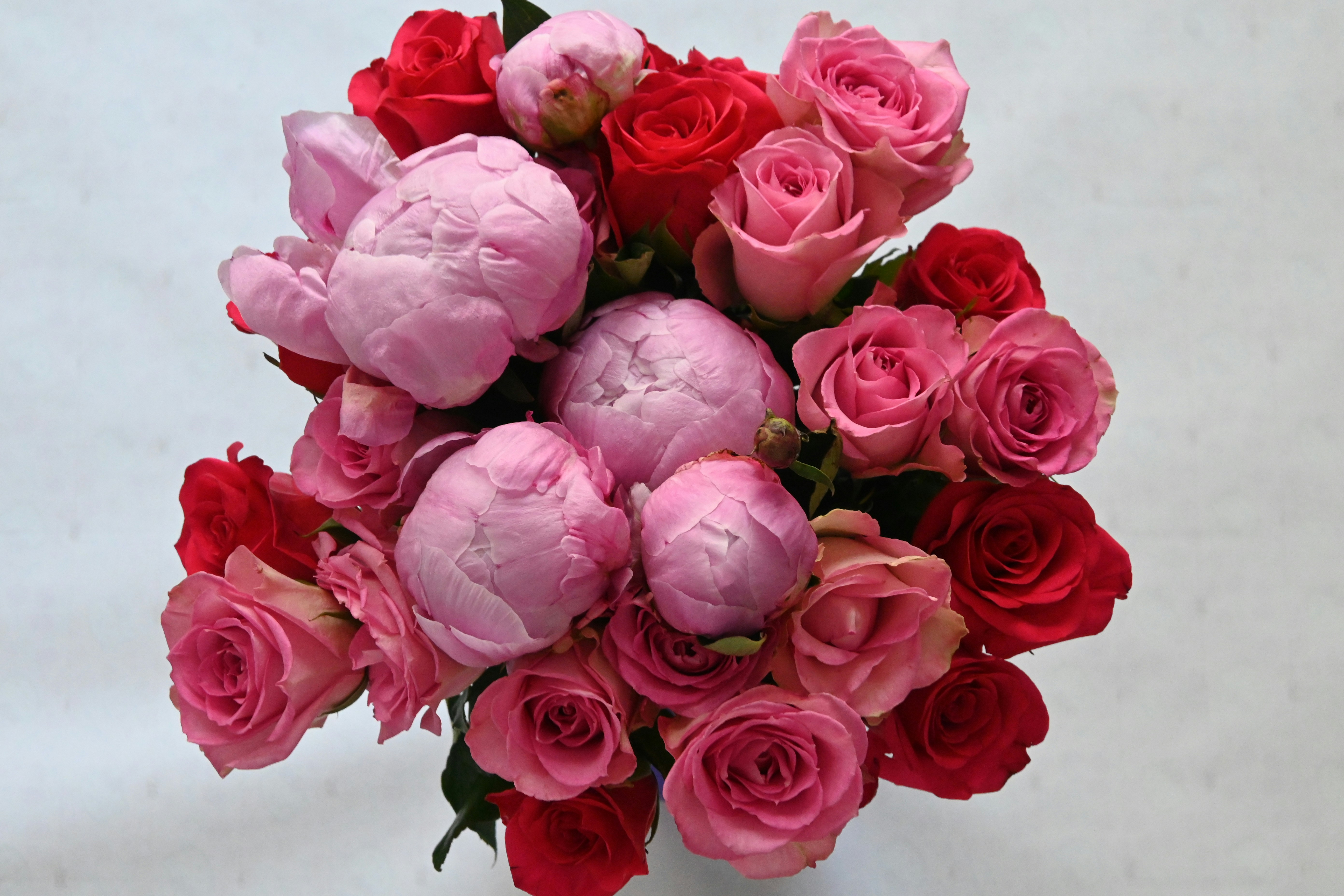 A tight bouquet of pink and red roses photographed from above, highlighting layered petals and a soft, pale backdrop. (Logo/branding not present.)