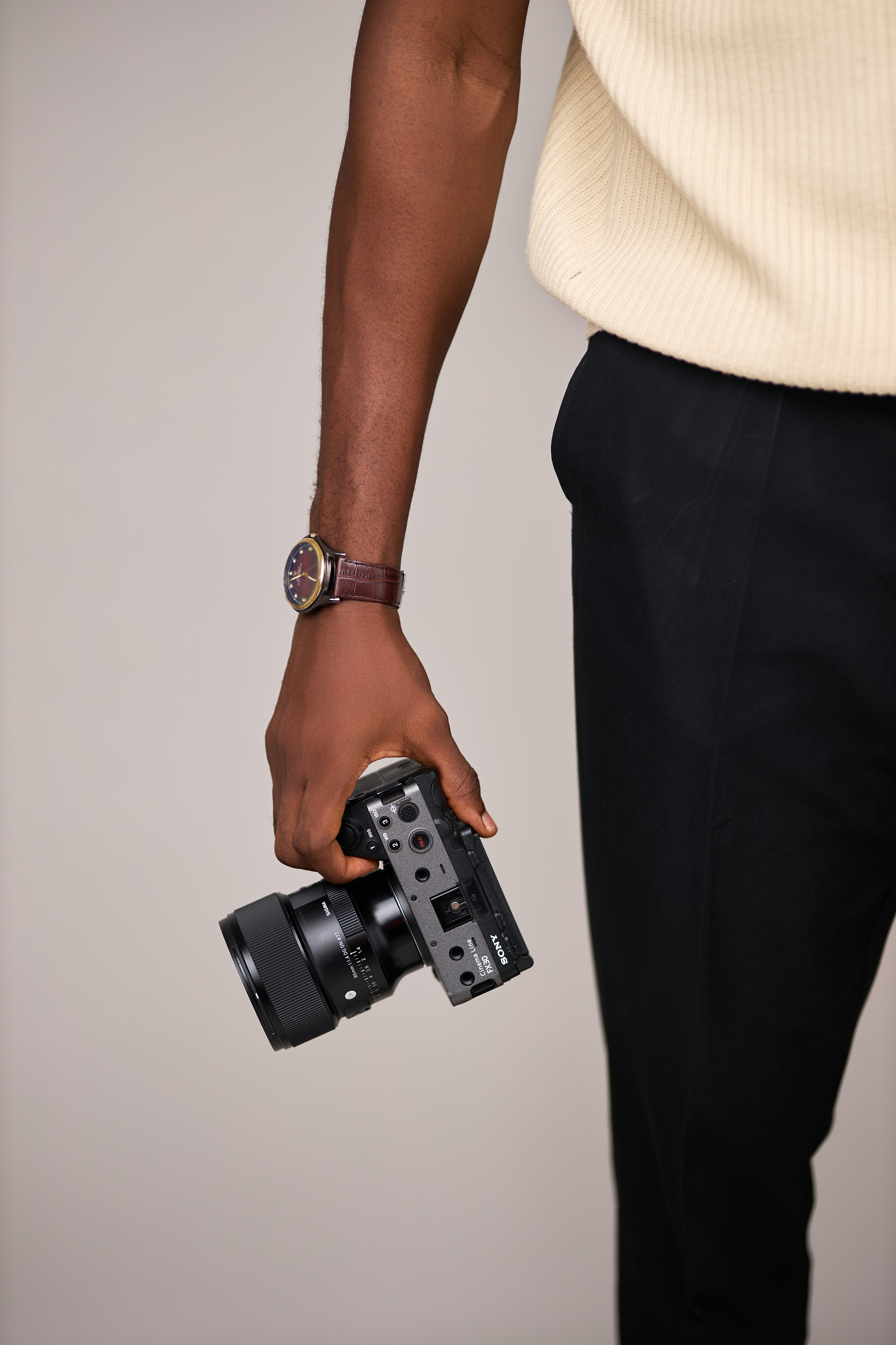 A person holding a black camera and wearing a watch.