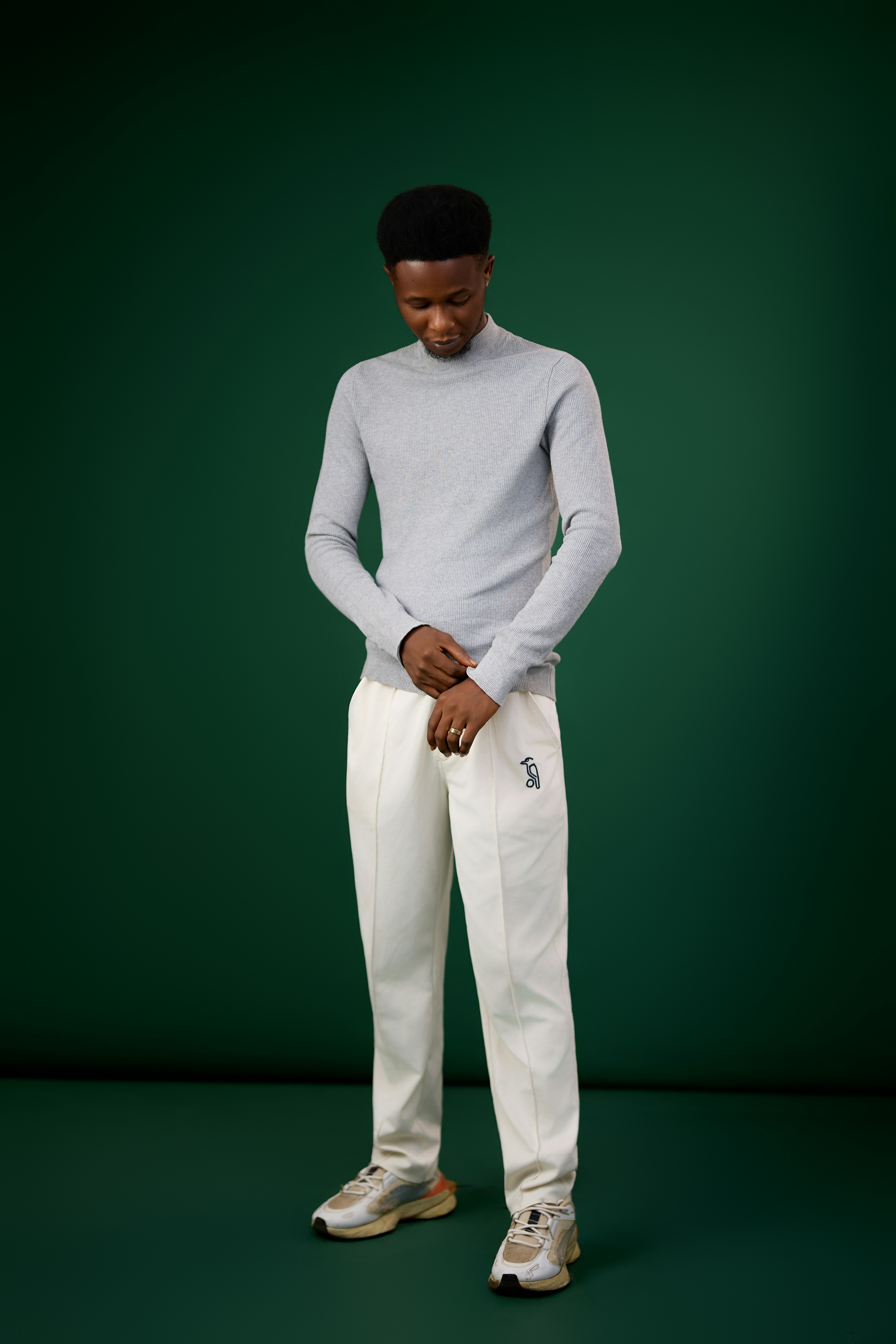 Man in grey turtleneck and white pants on green background.