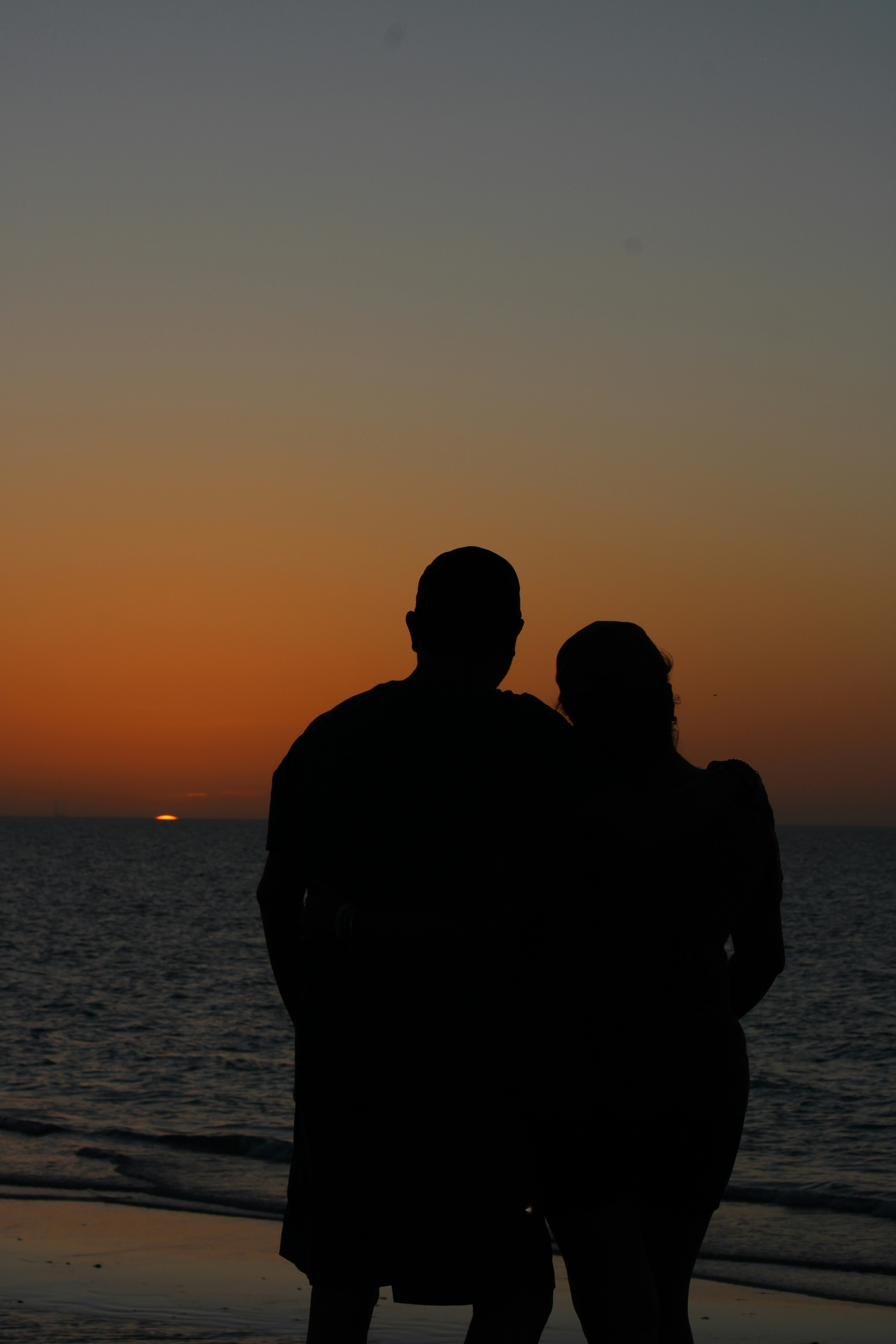 Silhouetted Anchor: Two Lovers at Sunset Over Calm Seas