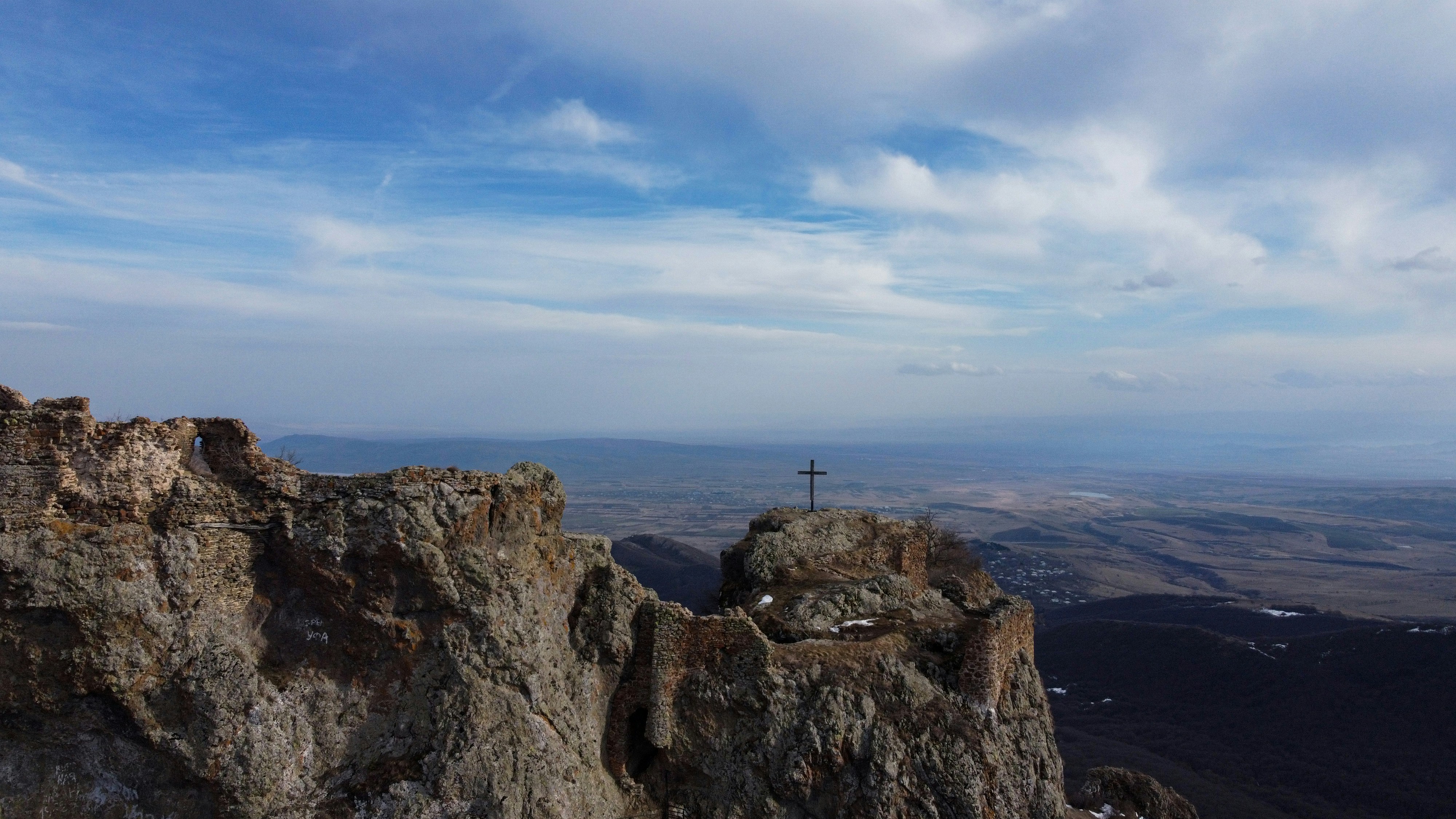 Cross atop the cliffs: distant valley and horizon anchored by a lone marker