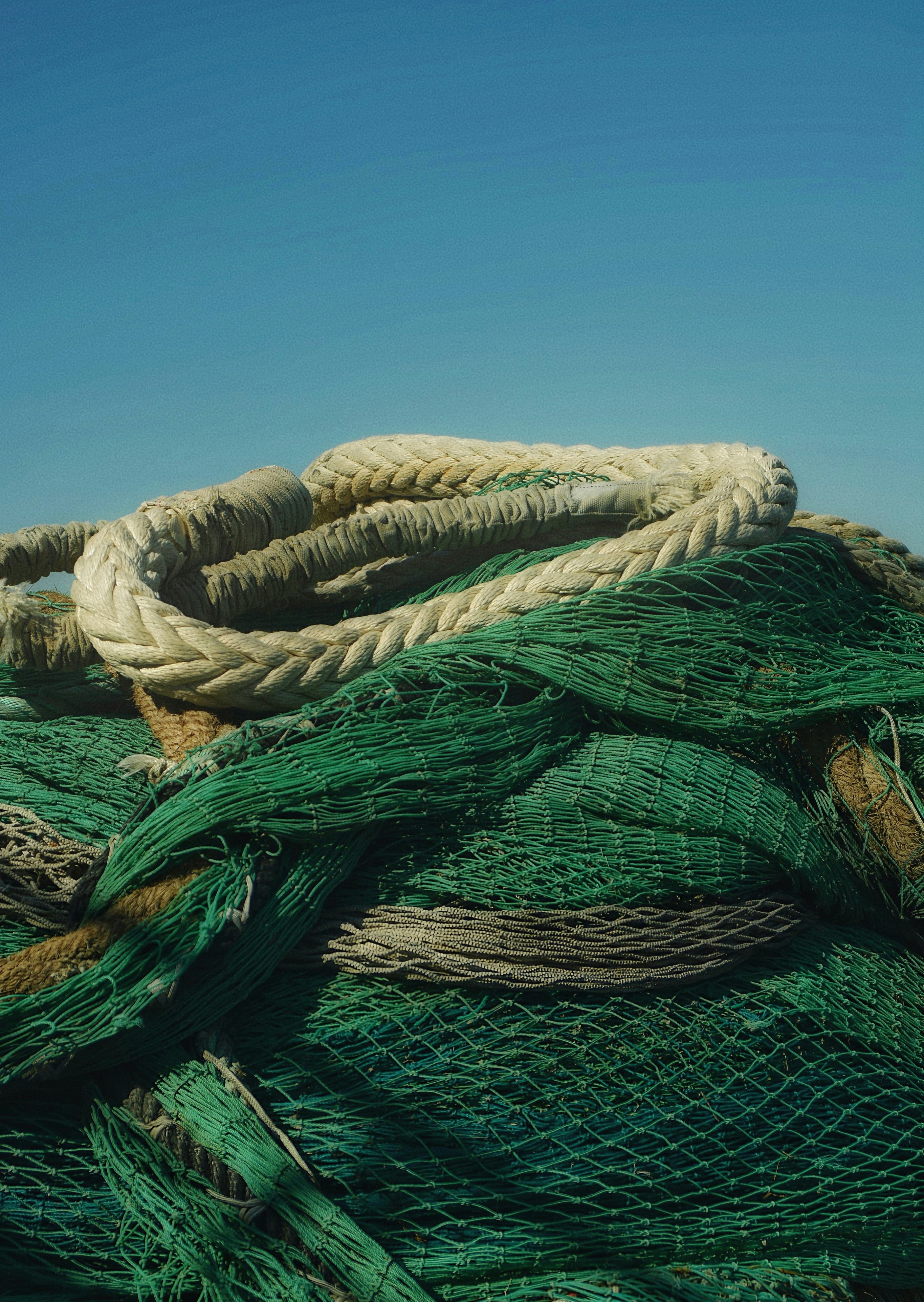 Tangled nets under a clear sky: ropes coiled atop green fishing nets