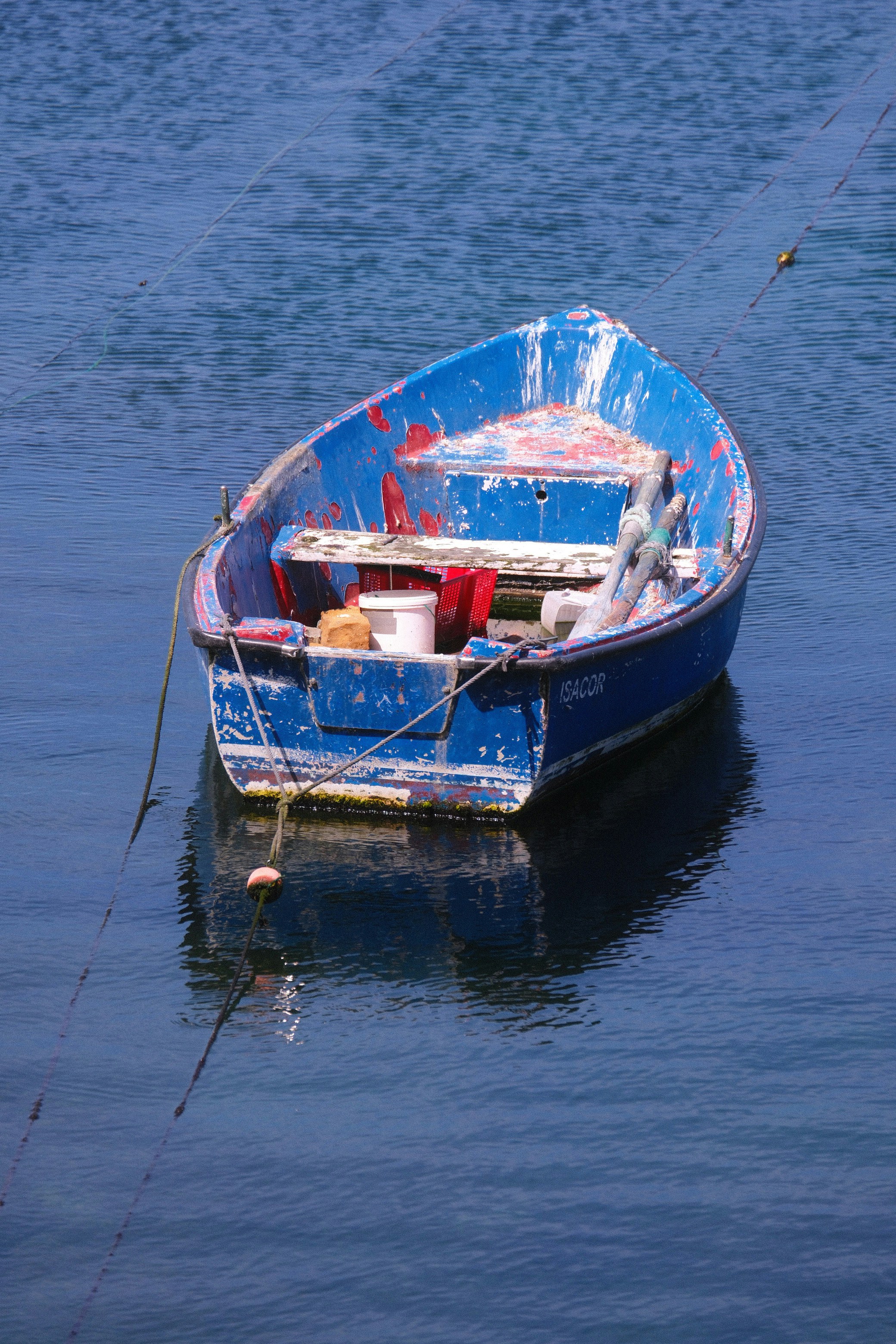 Blue rowboat anchored in calm harbor with weathered paint and supplies