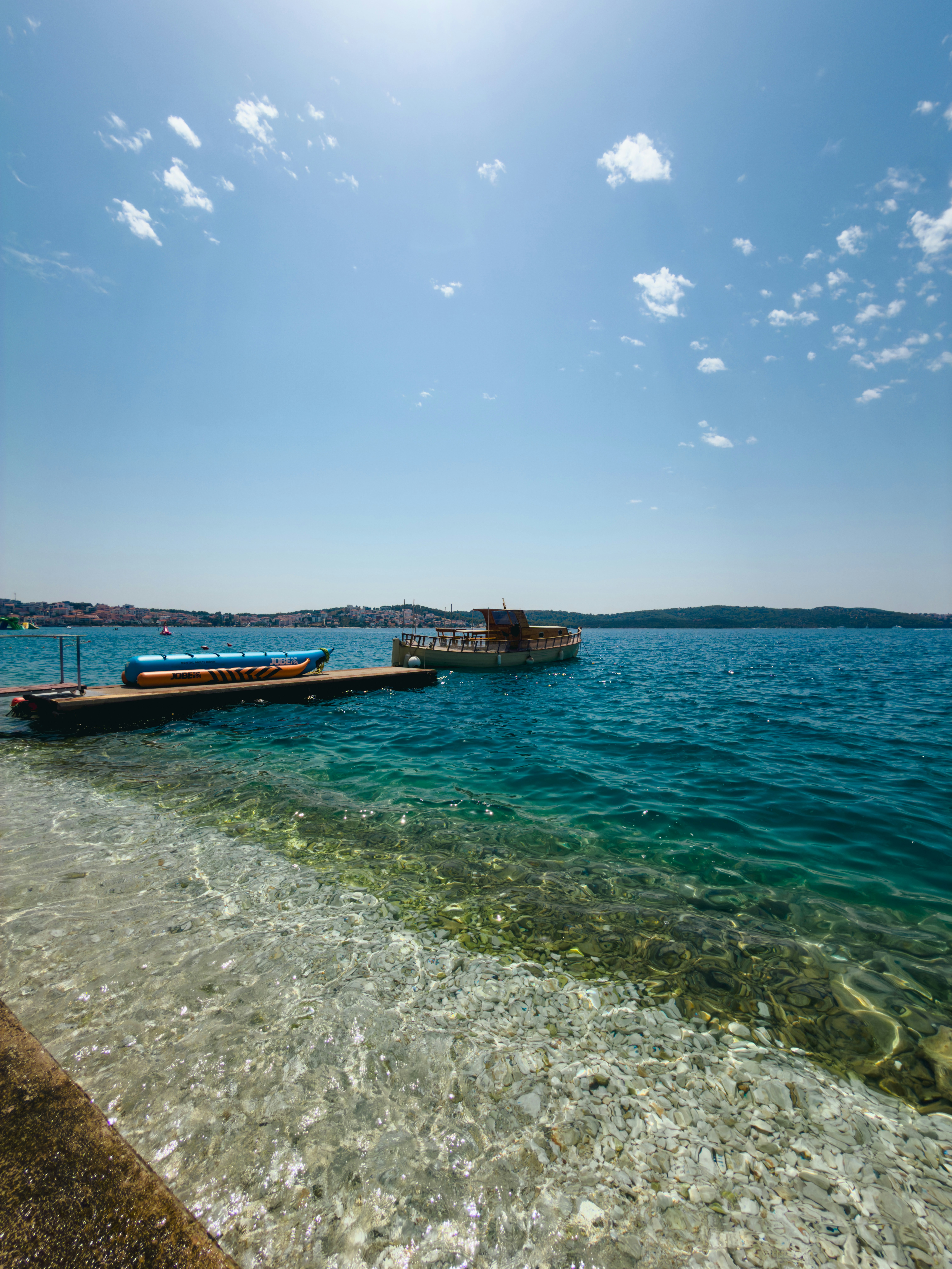 Bright coastal scene with small boats anchored near a rocky shore and turquoise water under a clear sky.