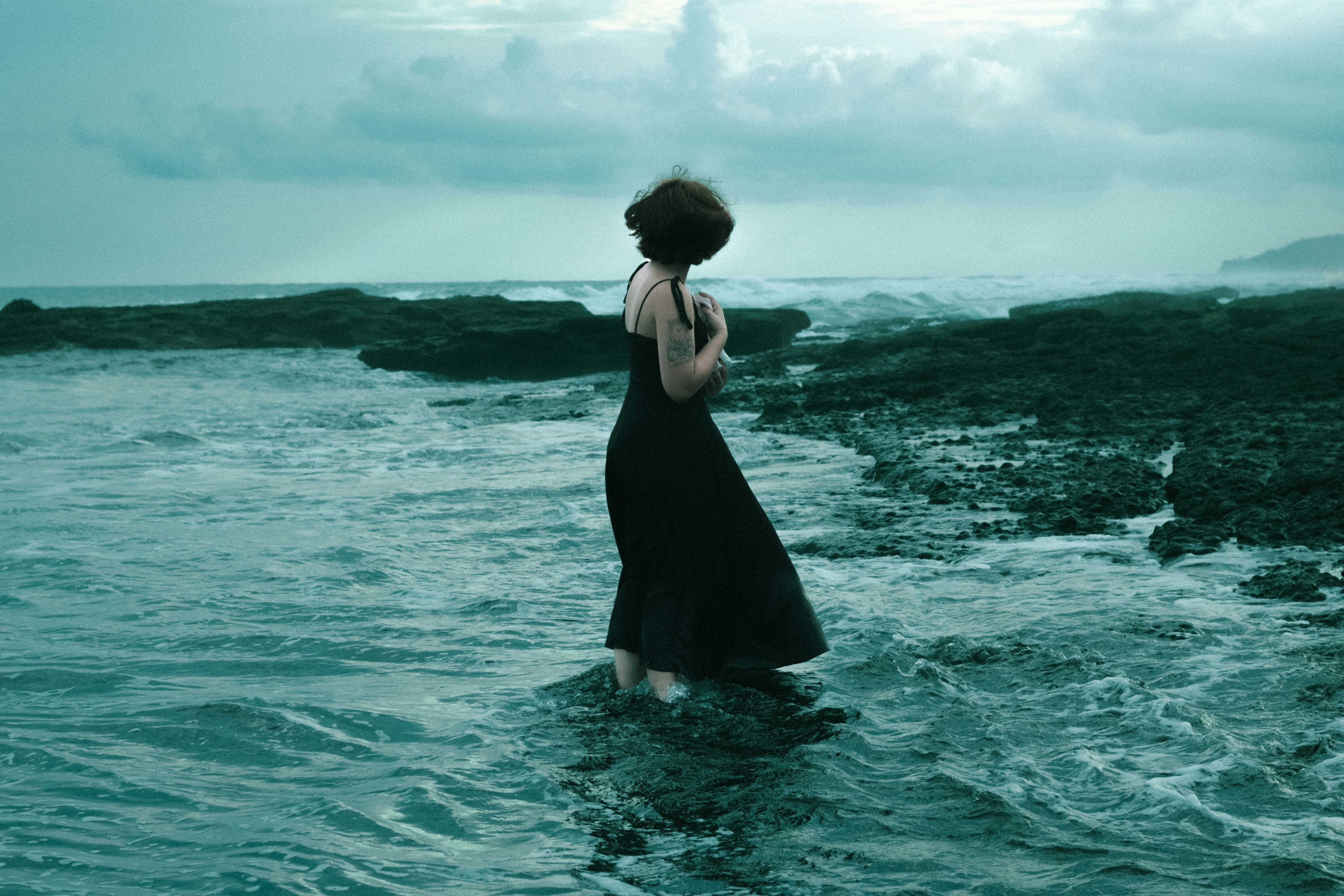  solitary figure in tidal silhouette stepping through sea-slick rocks at gloaming