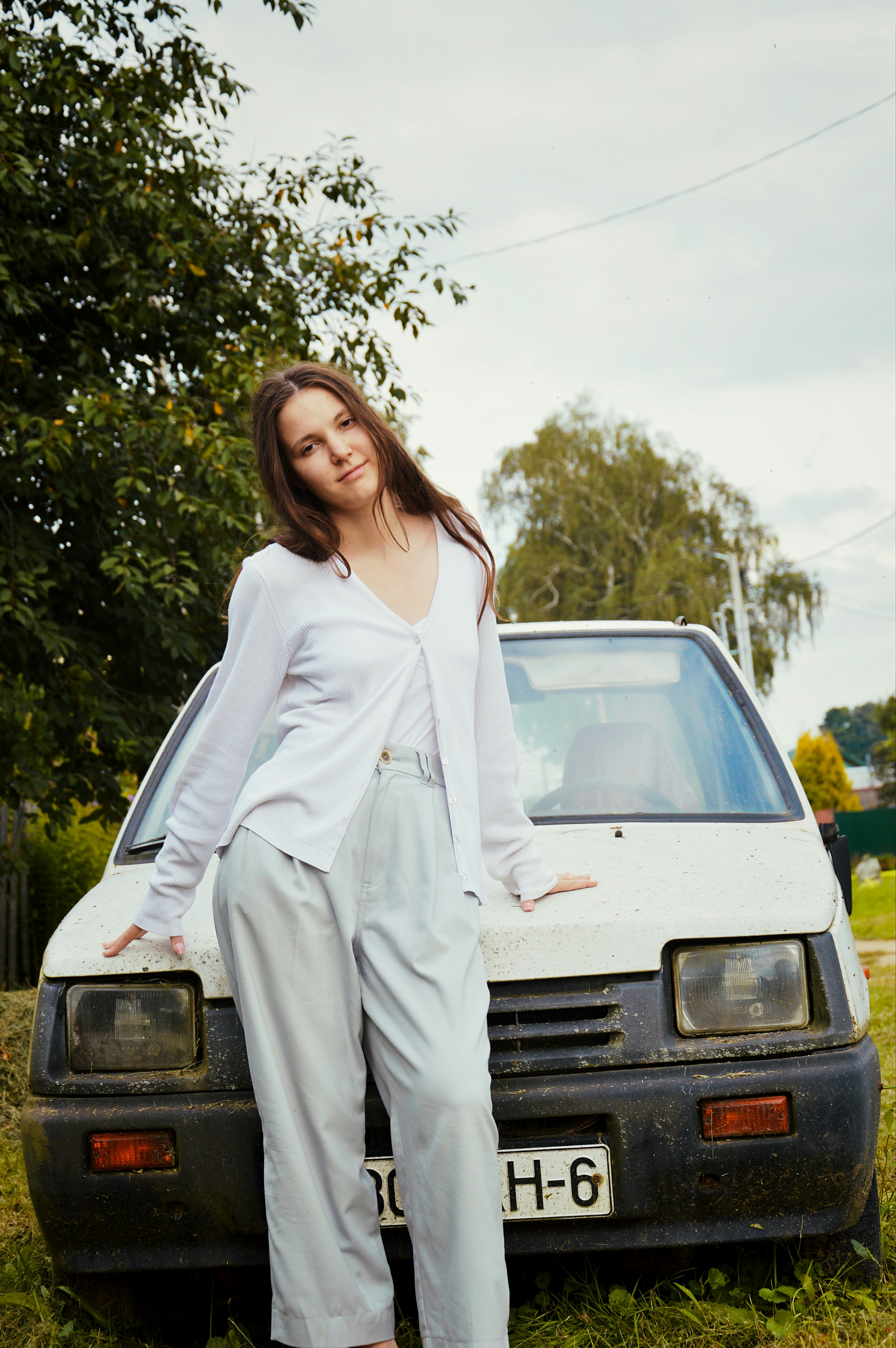 White-clad Portrait by a Weathered Car in Open Field
