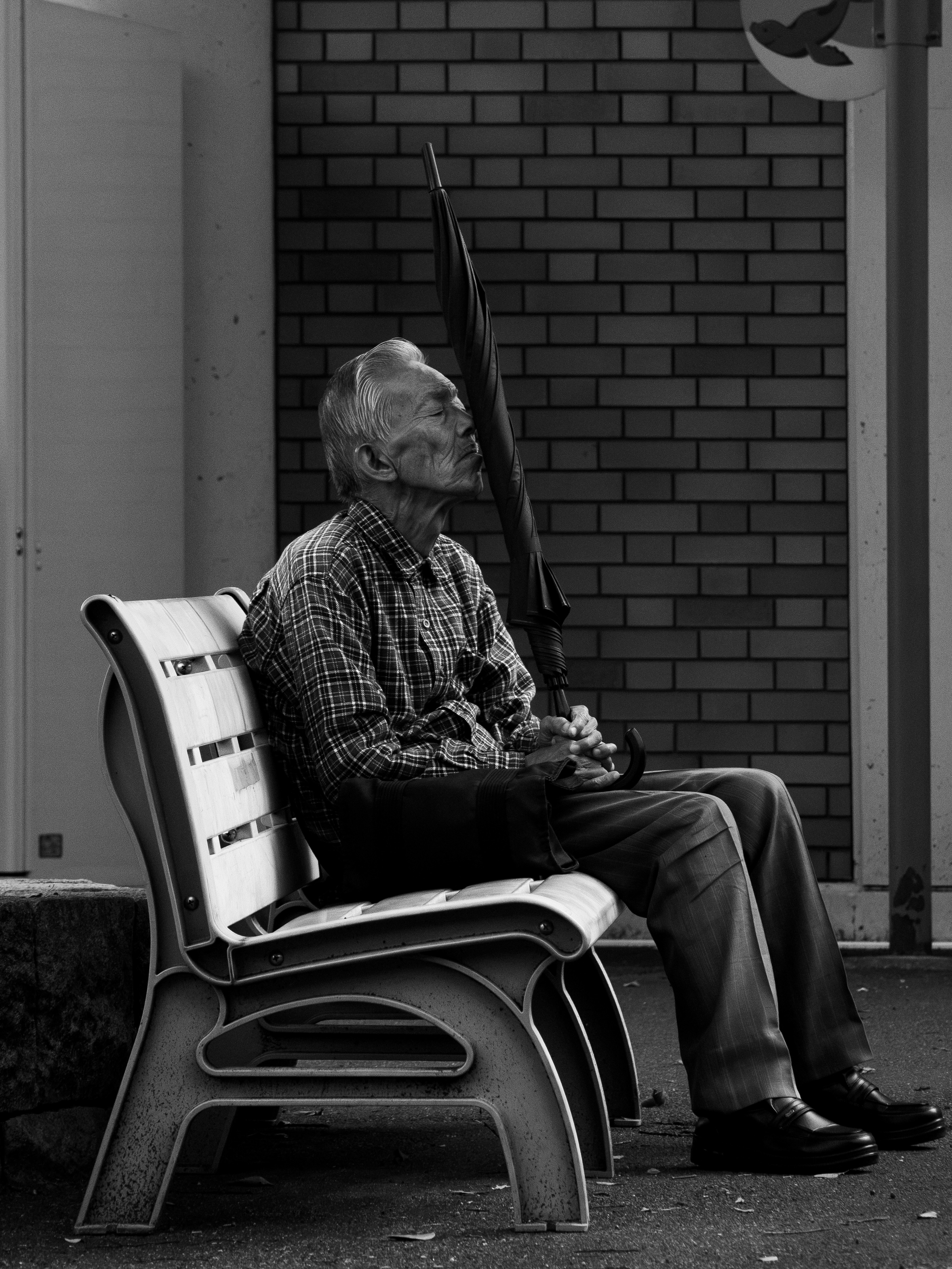 Silent Vigil: An Elder Seated with a Closed Umbrella in Quiet Urban Shade