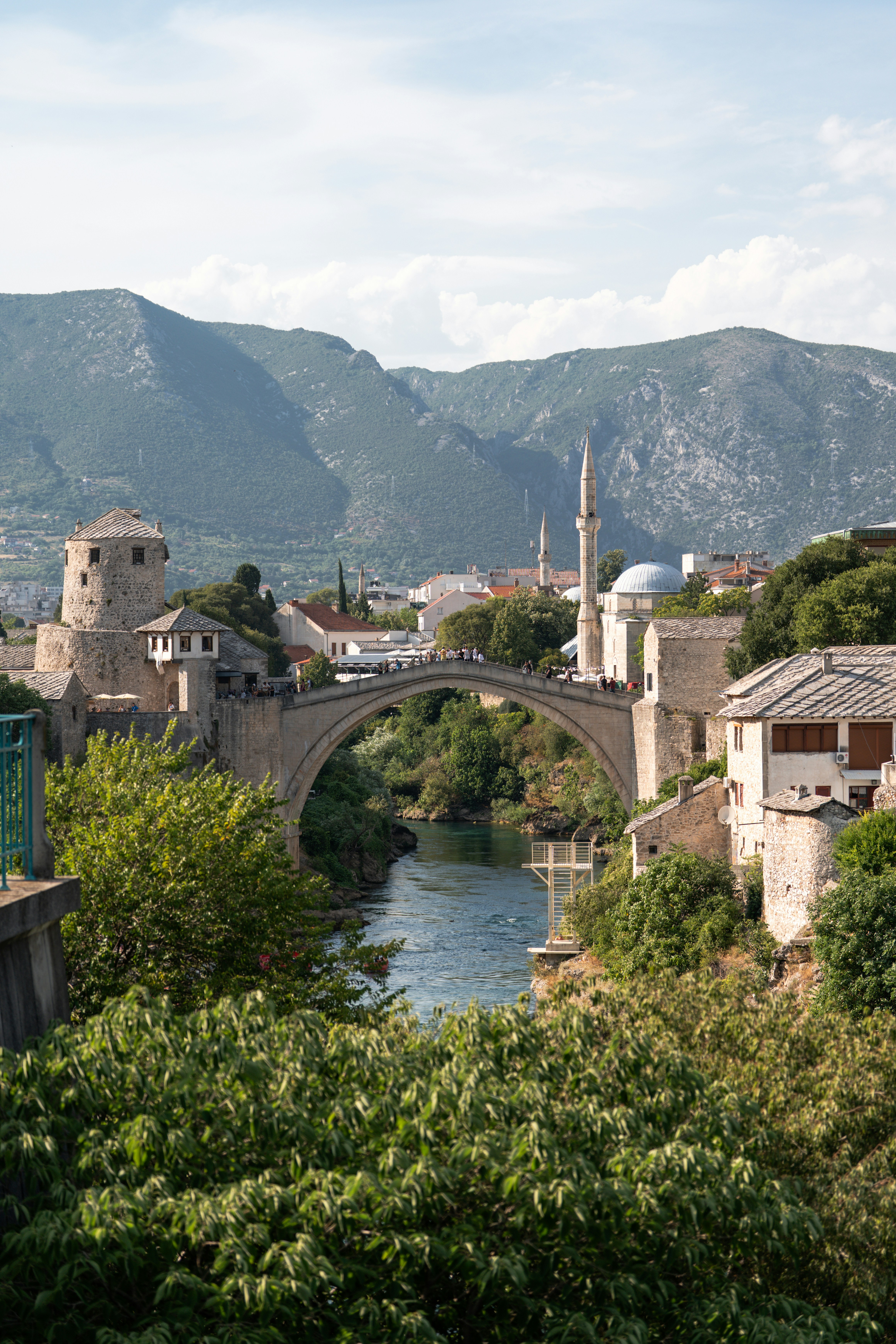 Ancient Stone Arch Over a Quiet River with Town and Mountains