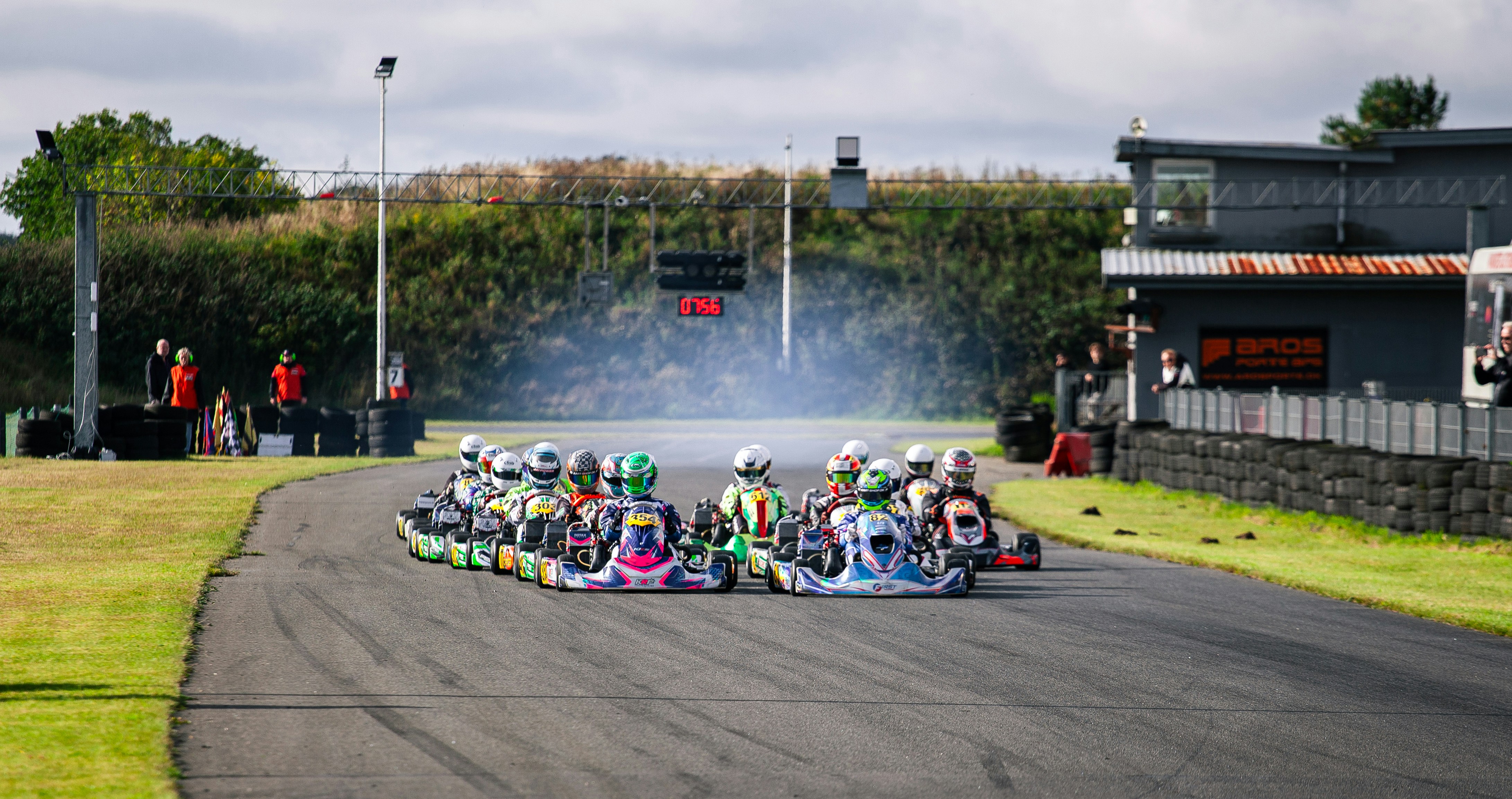 Leading Pack of Go-Karts Bunched at Turn Exit under a Smoke-Hazed Sky
