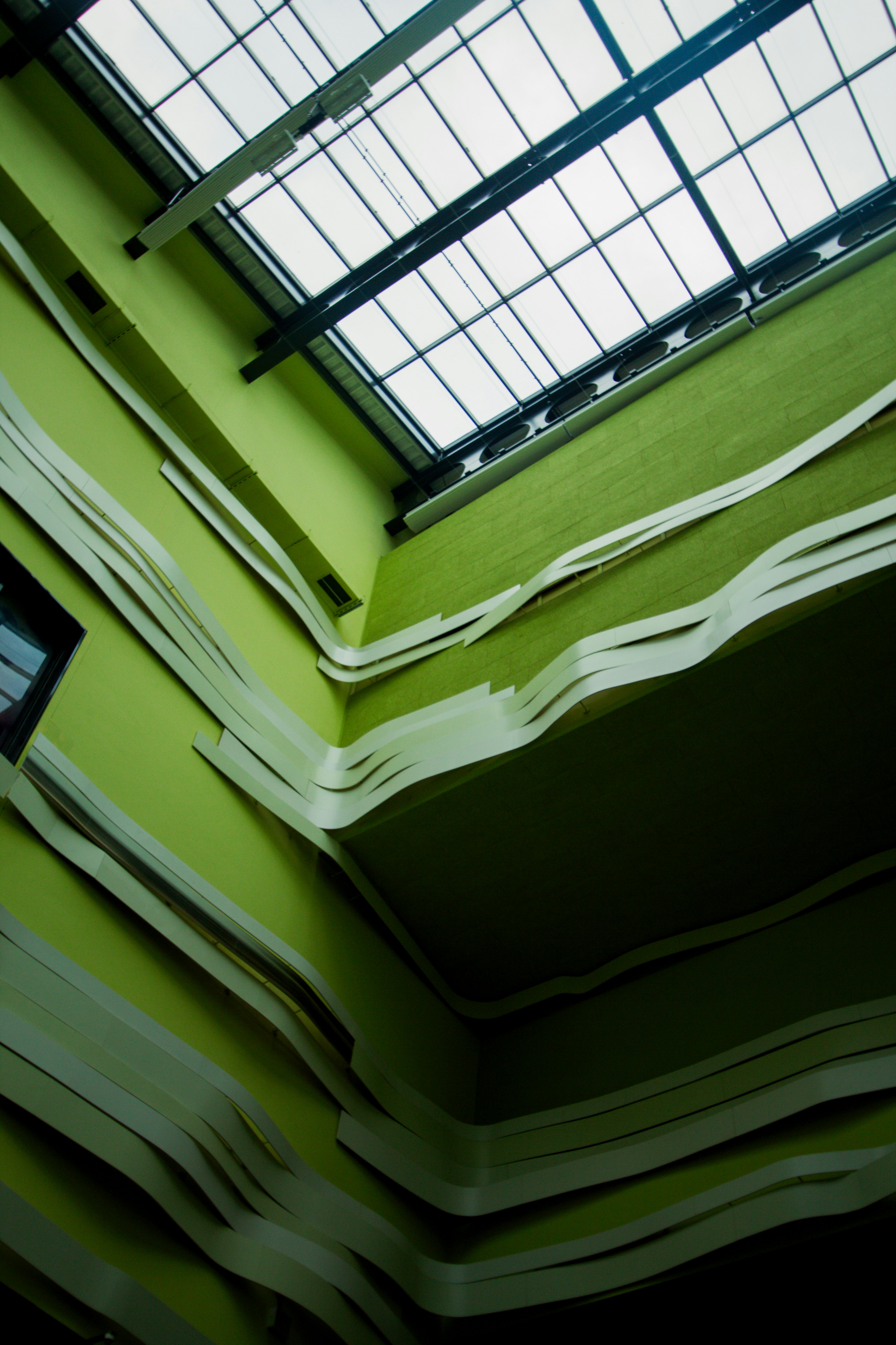 Vertical view of a lime-green interior with wavy white balconies and a glass ceiling, creating a modern architectural composition.