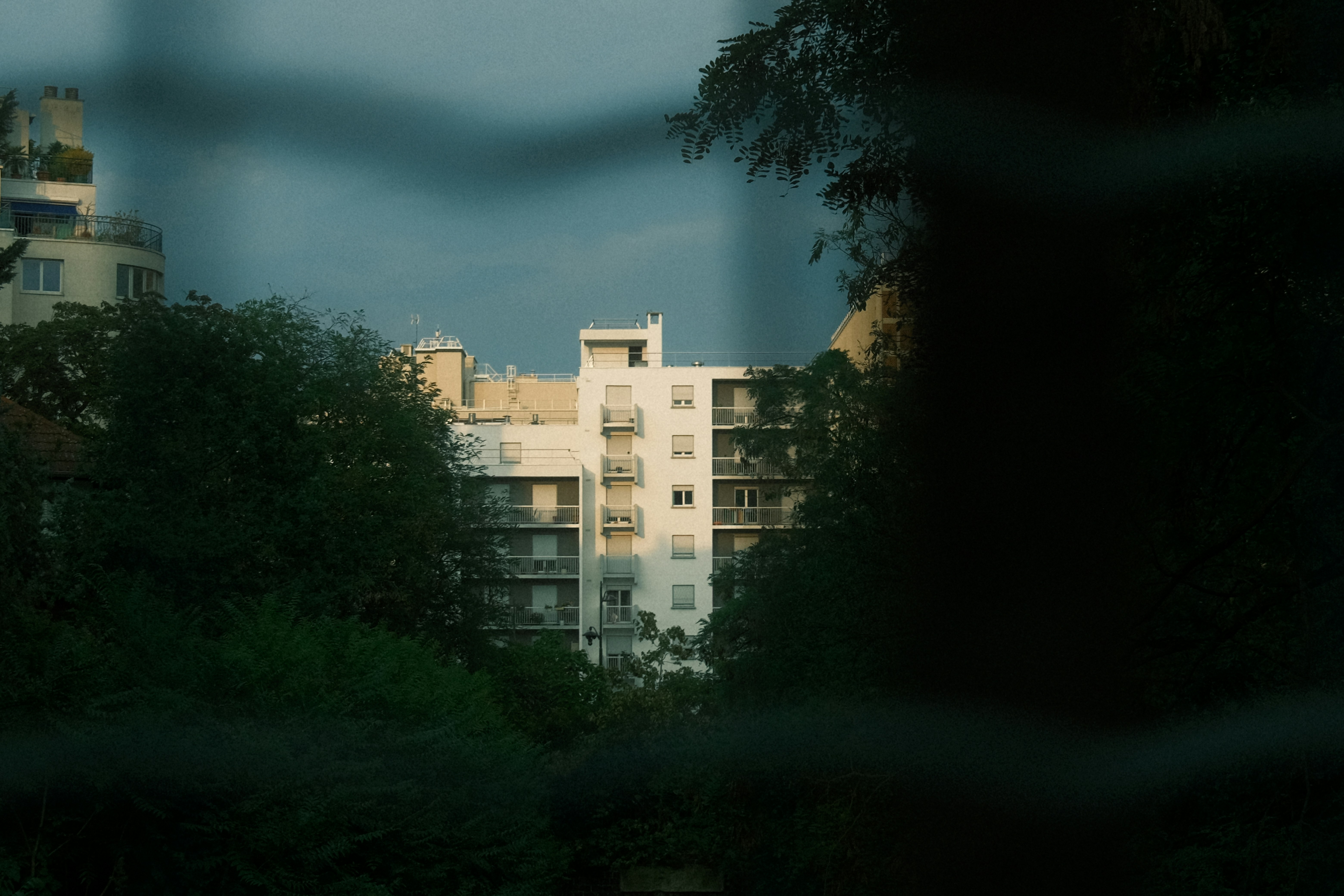 Distant building framed by dark foreground bars, revealing a residential facade bathed in soft daylight.