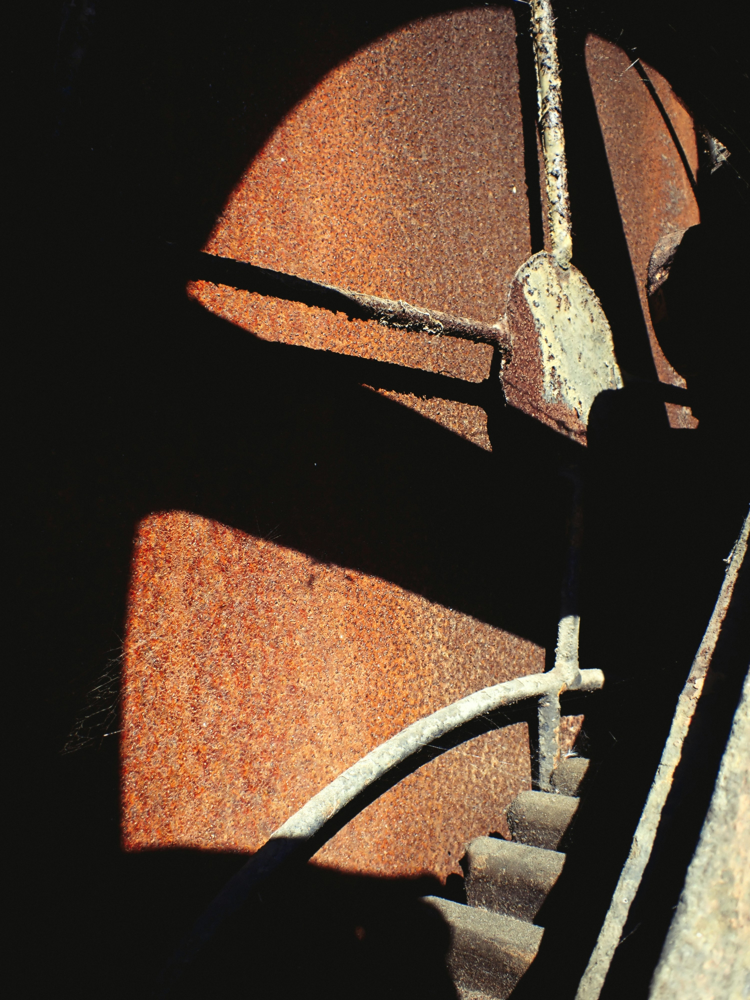 Rusty industrial forms wrapped in deep shadows, revealing a curved rail and angular metal pieces in a stark, high-contrast composition.