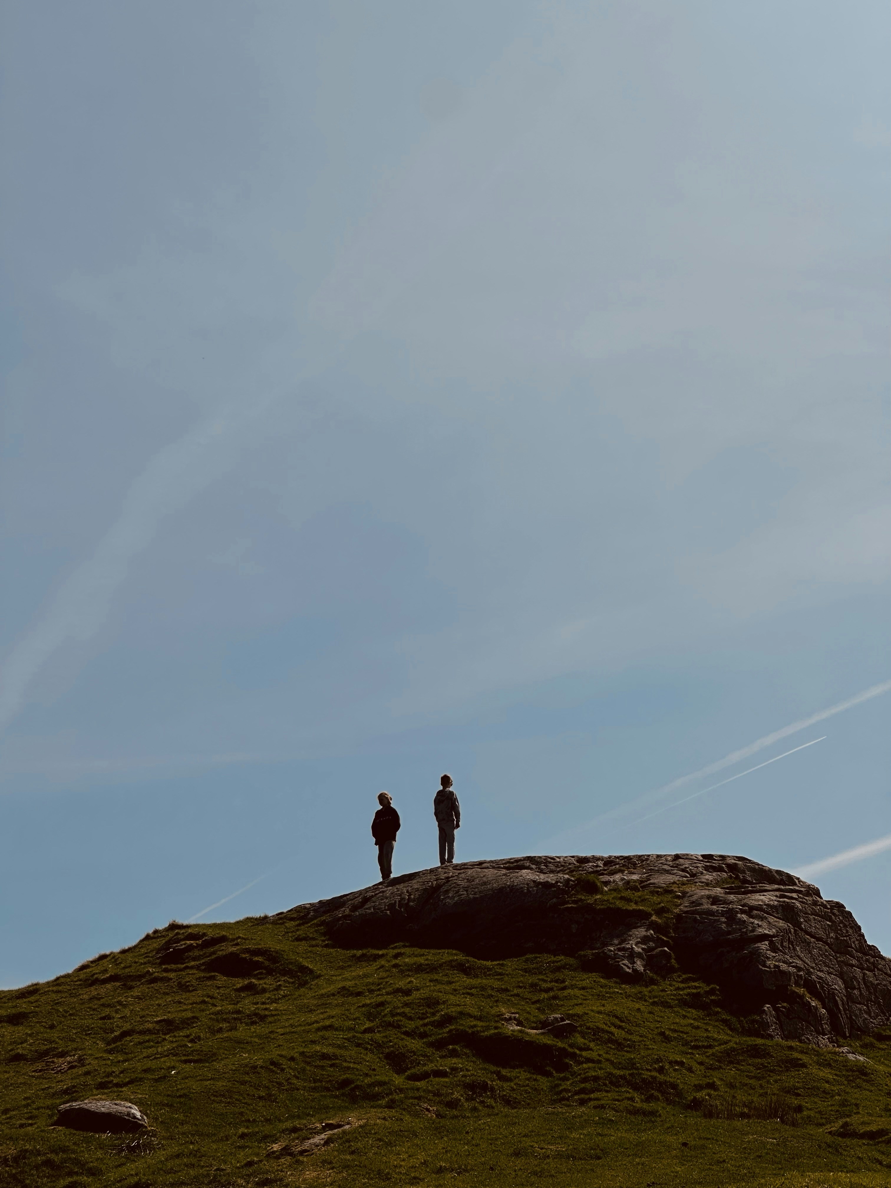 Two Silhouettes atop a grassy ridge under a wide blue sky